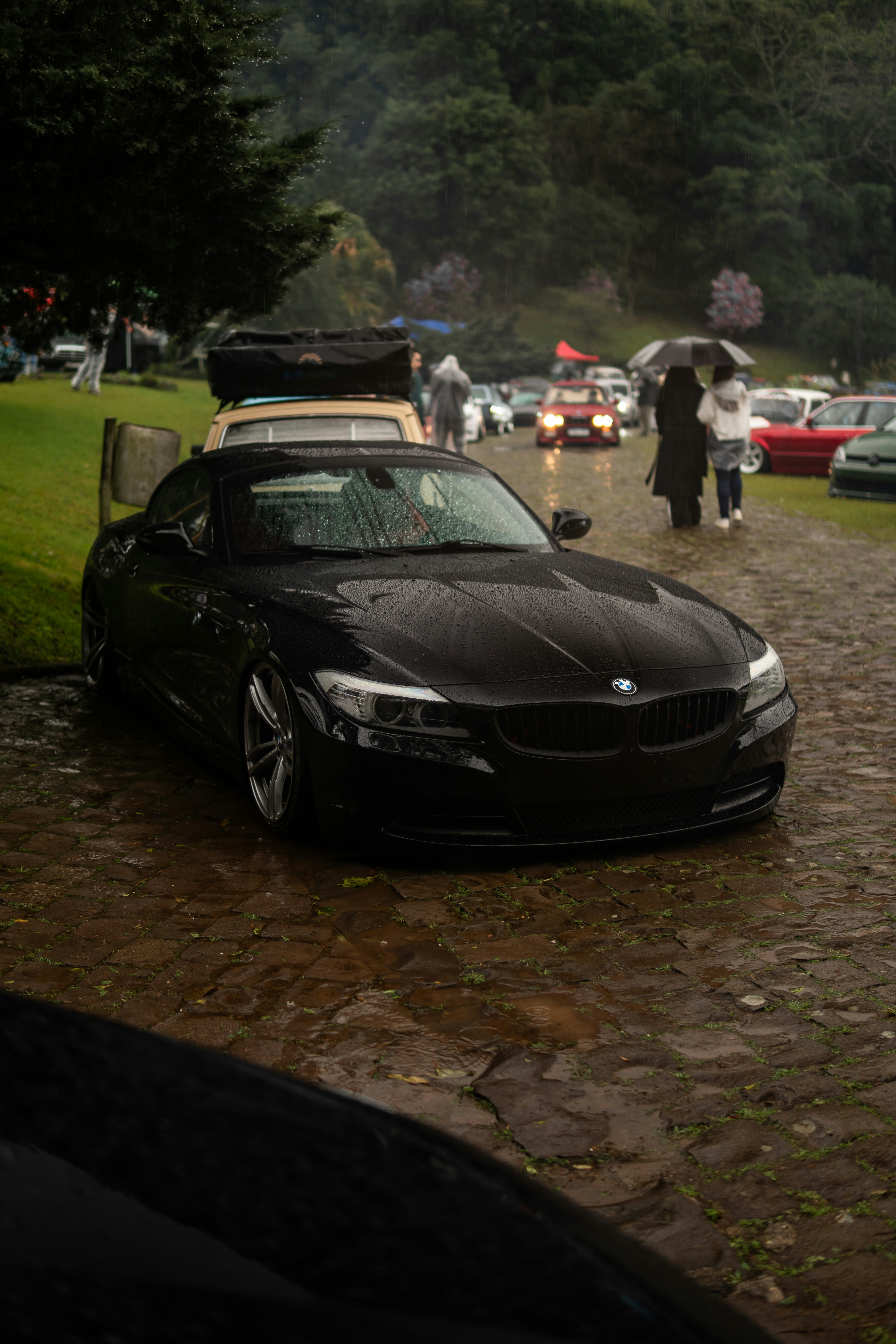 Low-Glare Black BMW on a Rainy Cobblestone Path at a Car Meet