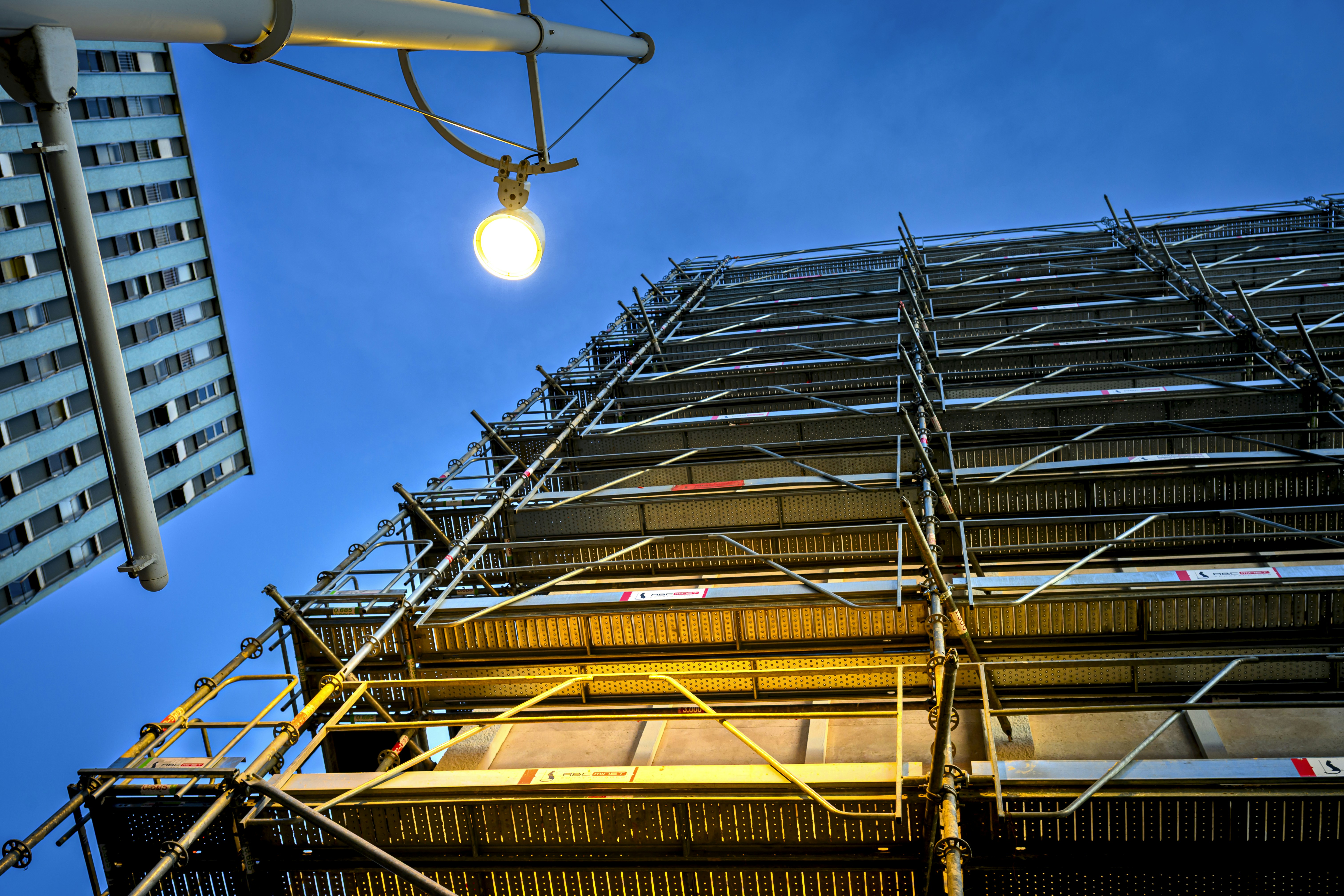 Scaffolding enveloping a building under construction, illuminated by a streetlight against a twilight sky.