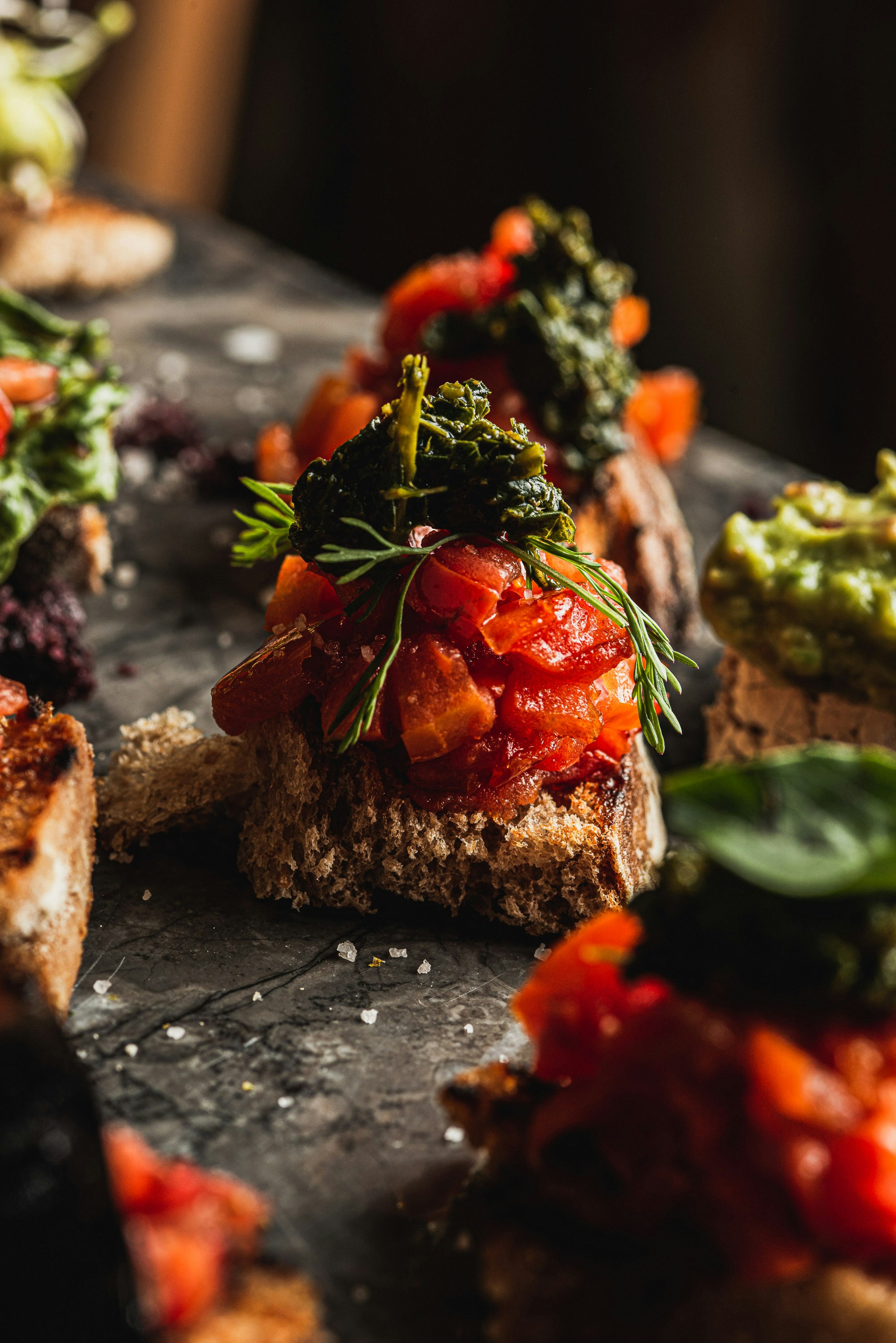 Artfully arranged canapés topped with vibrant vegetables and herbs on rustic bread, showcasing culinary creativity.