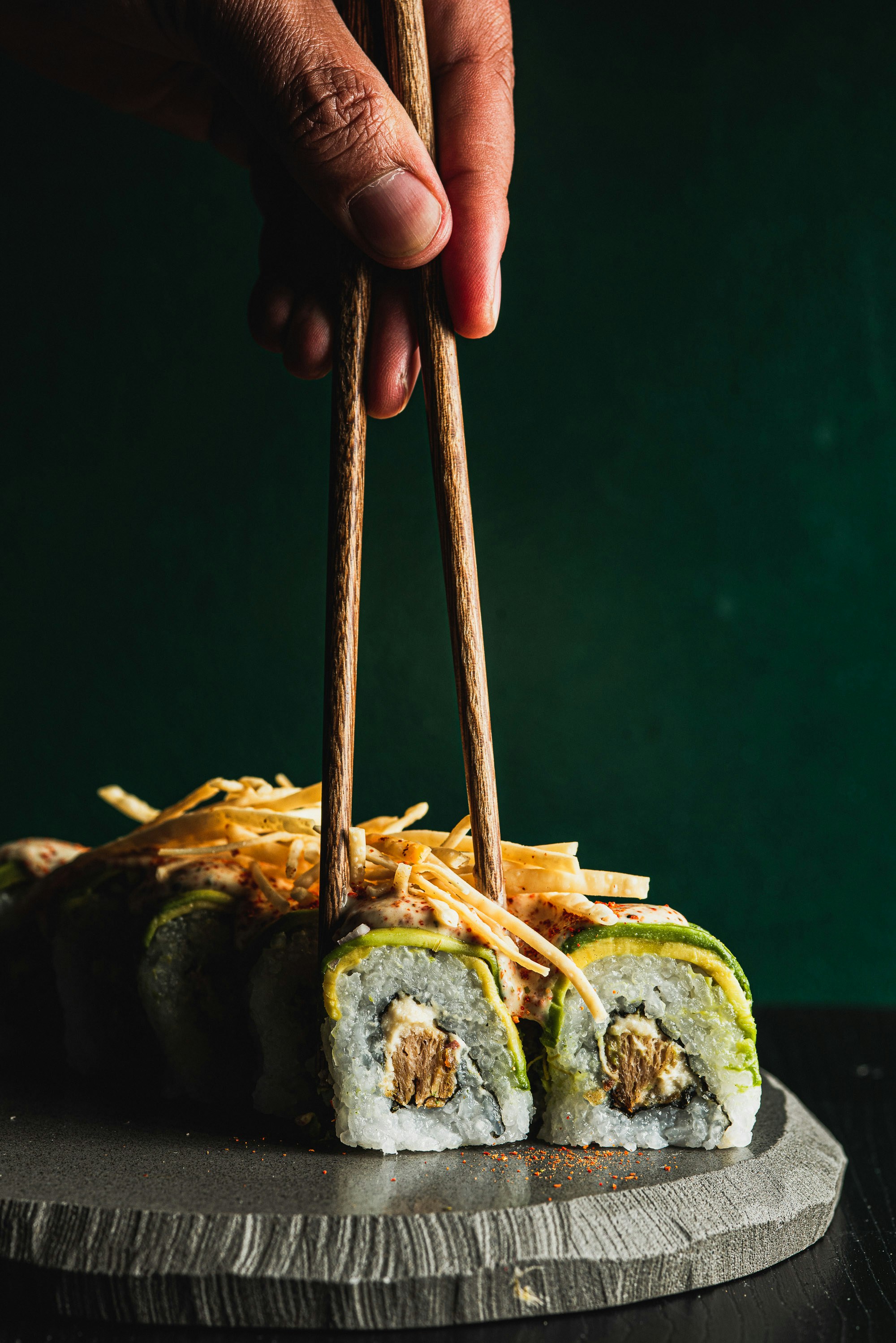 Crunchy Sushi Roll Gripped by Chopsticks on a Dark Slate Plate