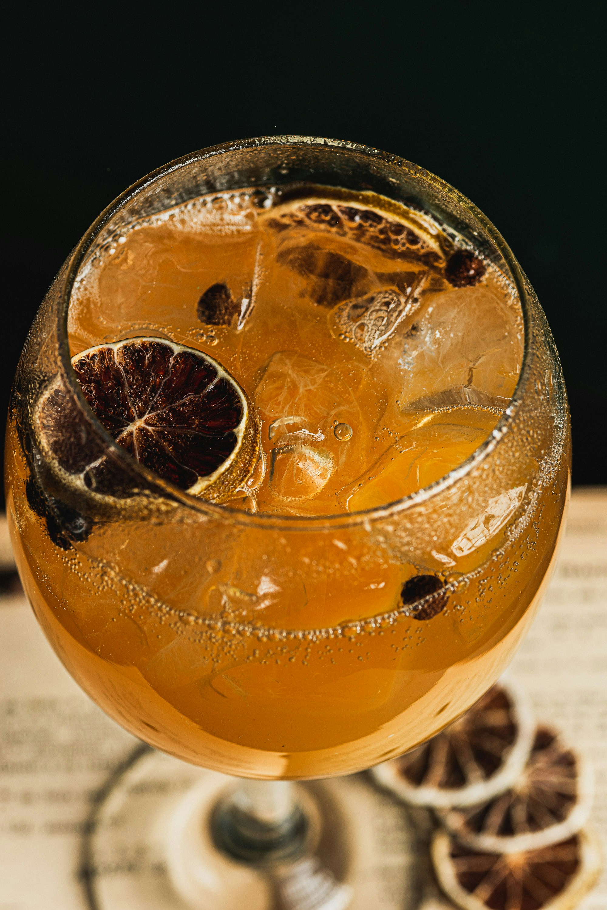 A refreshing cocktail featuring dried citrus slices and ice, served in a crystal glass. The drink is placed on a textured surface, enhancing its vibrant colors.