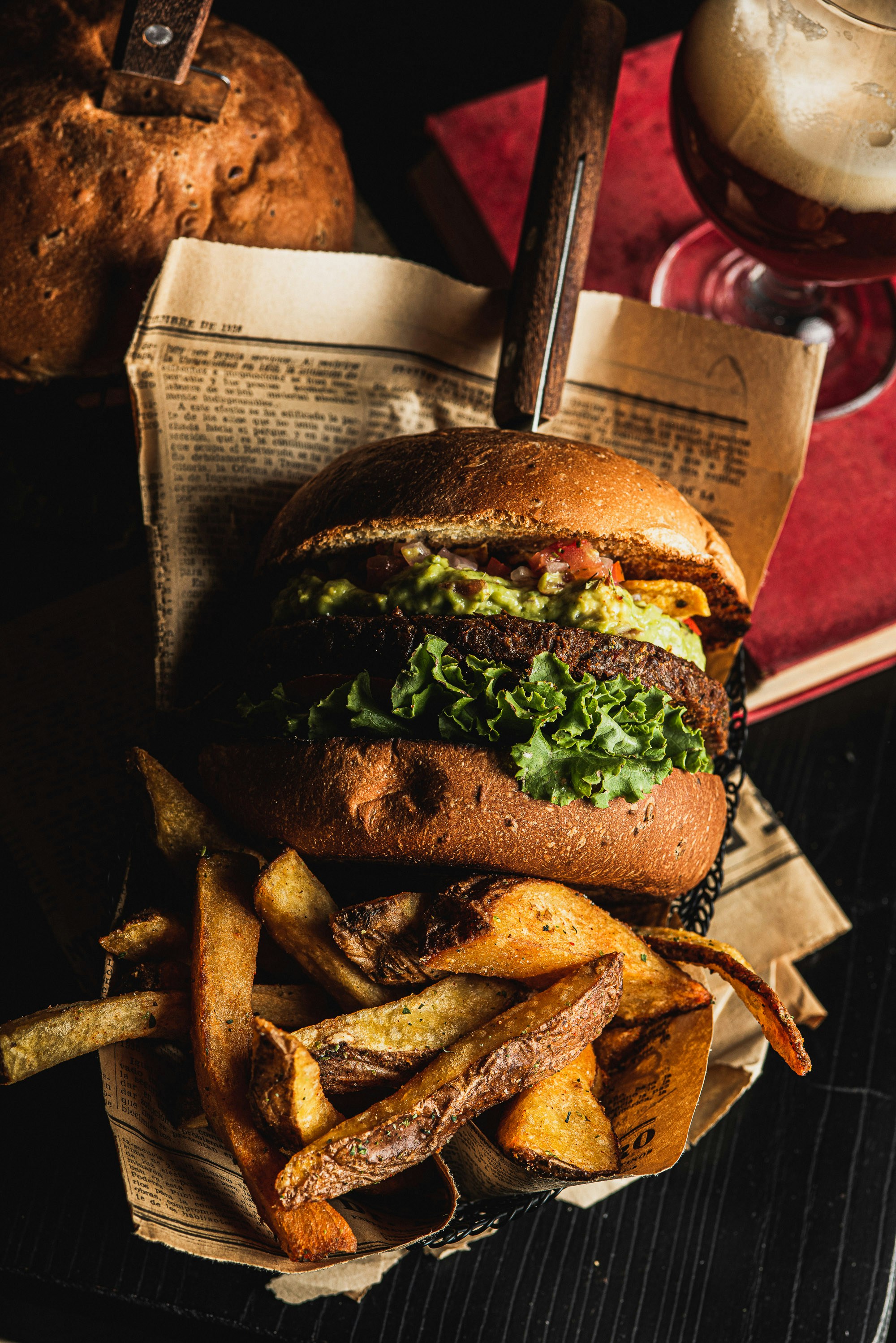 Juicy gourmet burger layered with fresh lettuce, tomatoes, and guacamole, served with crispy fries on a vintage newspaper backdrop.