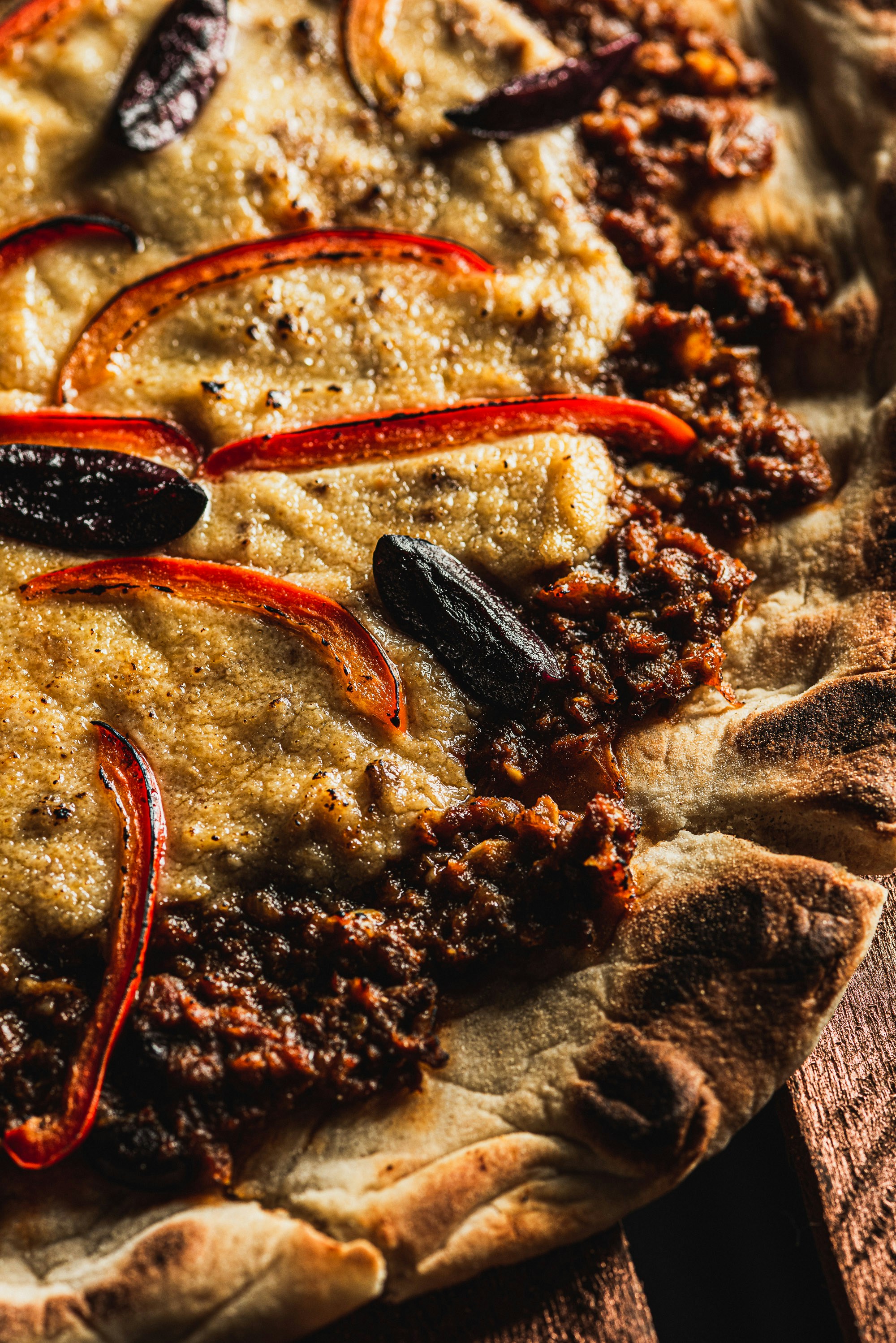 Close-up of a gourmet pizza topped with rich meat, cheese, and vibrant red pepper slices, showcasing a golden crust. 