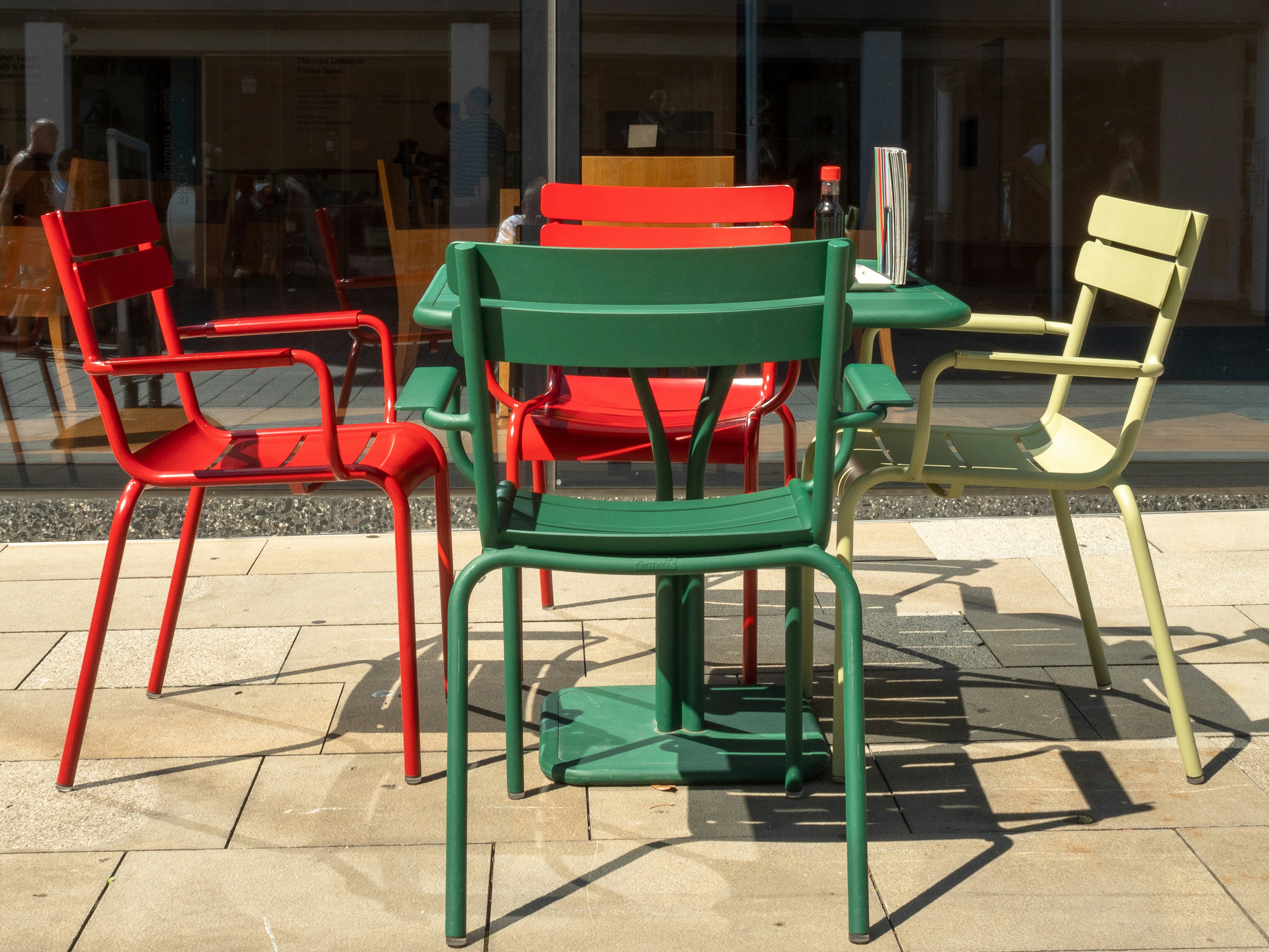Gartenstühle warten auf Gäste. | Colorful metal chairs and table on pavement
