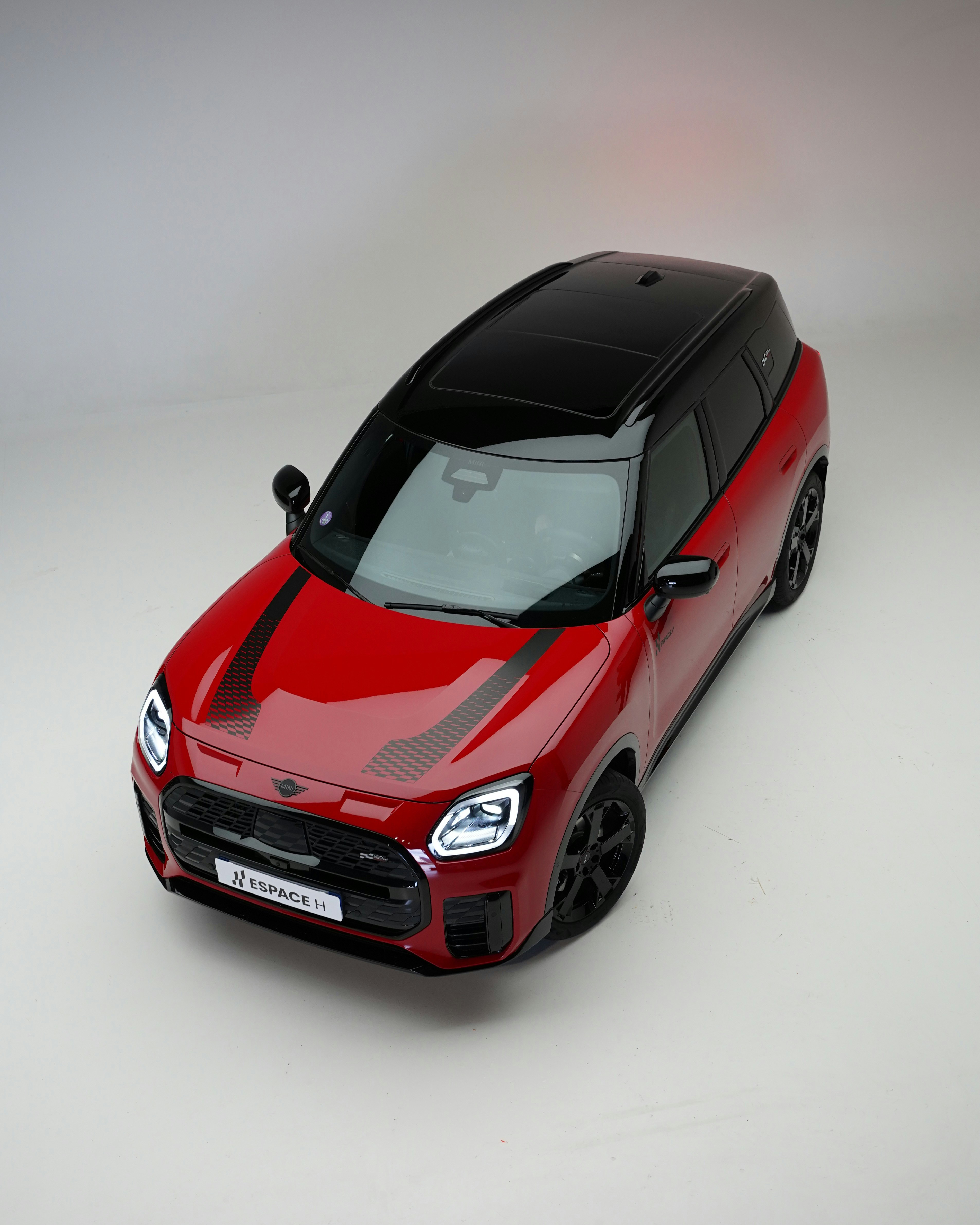 A sleek red car with a black roof, showcasing modern design elements against a neutral background. The vehicle's sporty features and distinctive branding are prominently displayed.