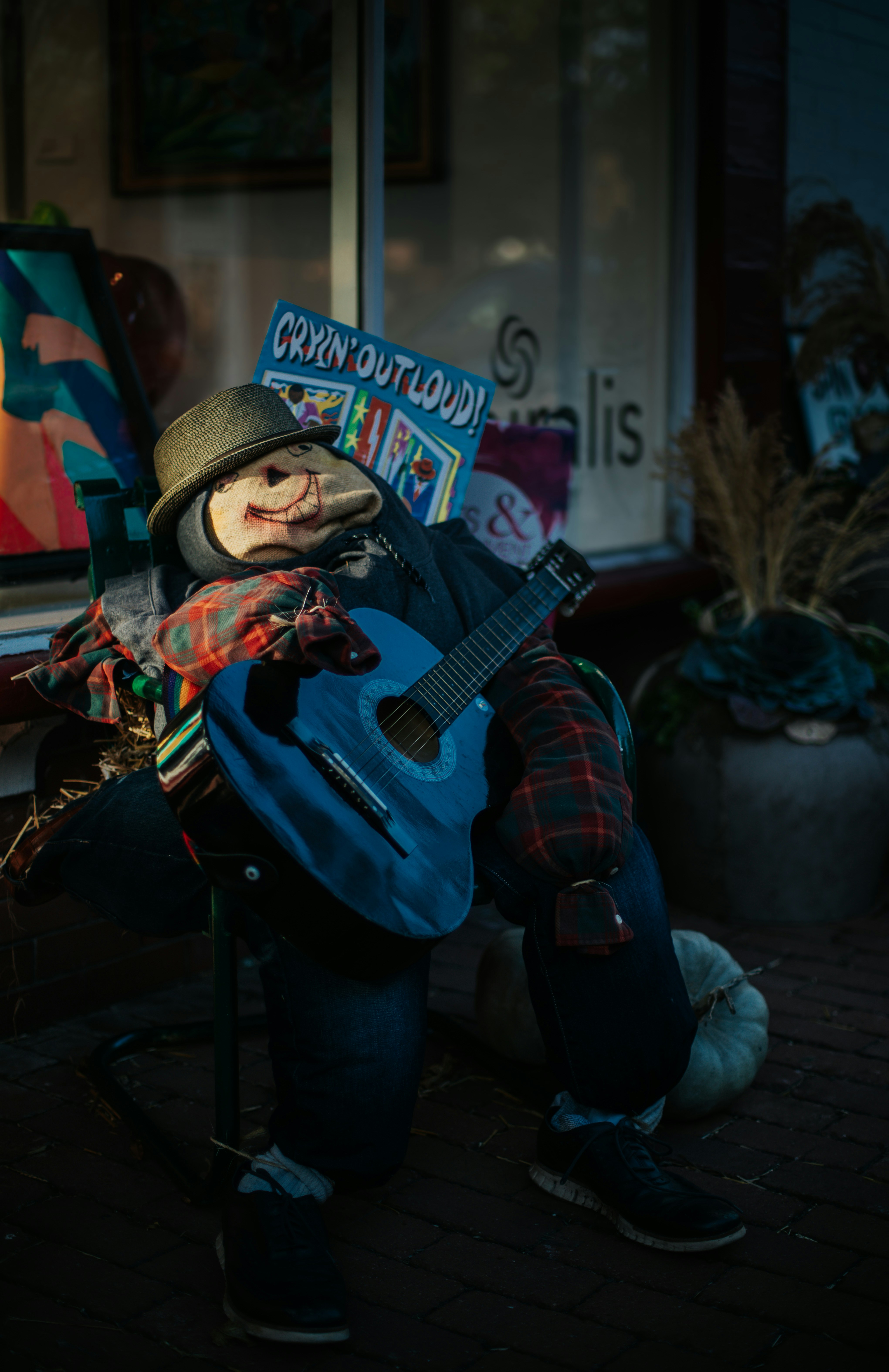 Scarecrow with hat playing blue guitar outside store
