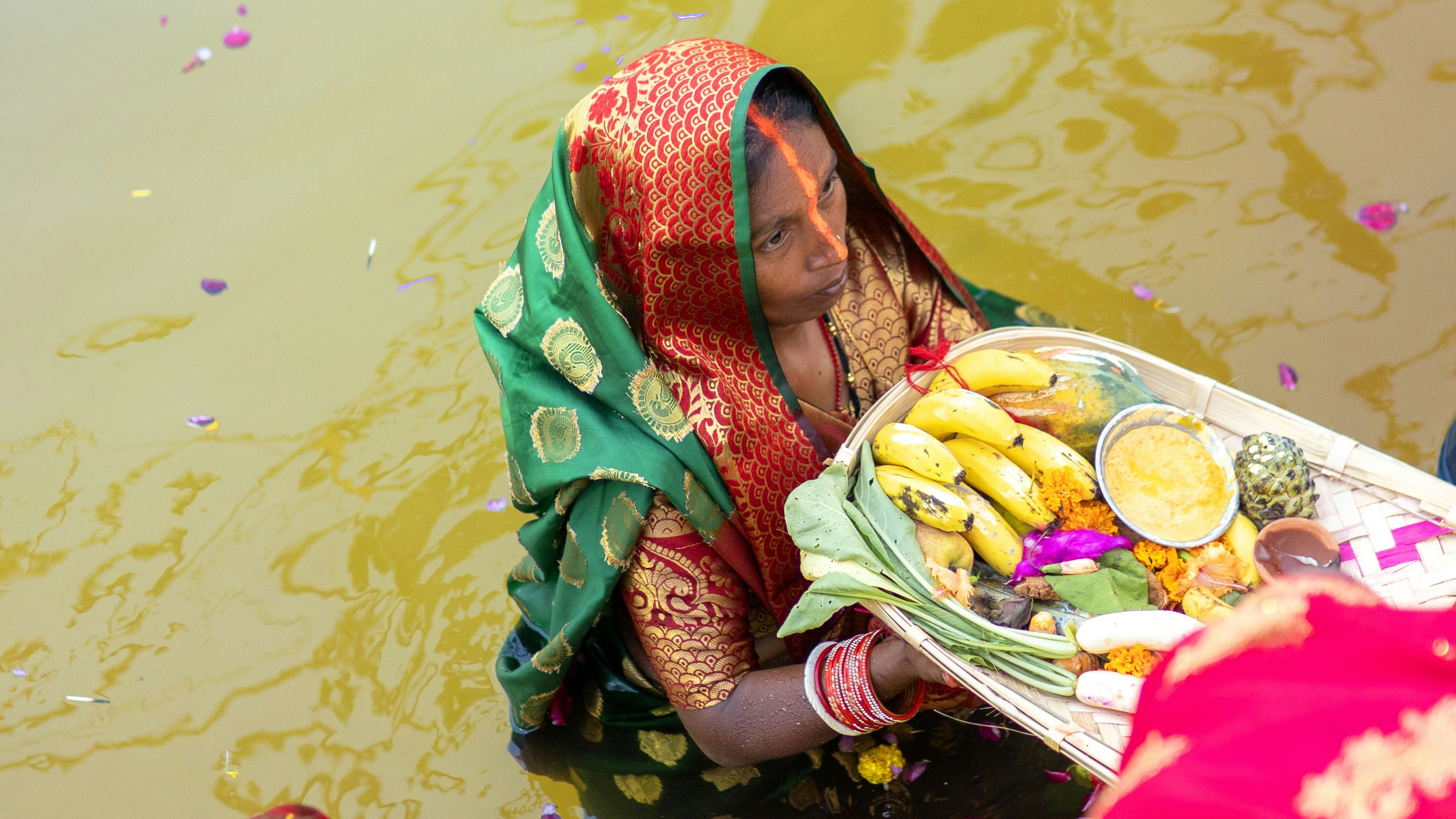 A woman offers arghya with fruits and diyas during Chhath Puja to worship the rising sun.