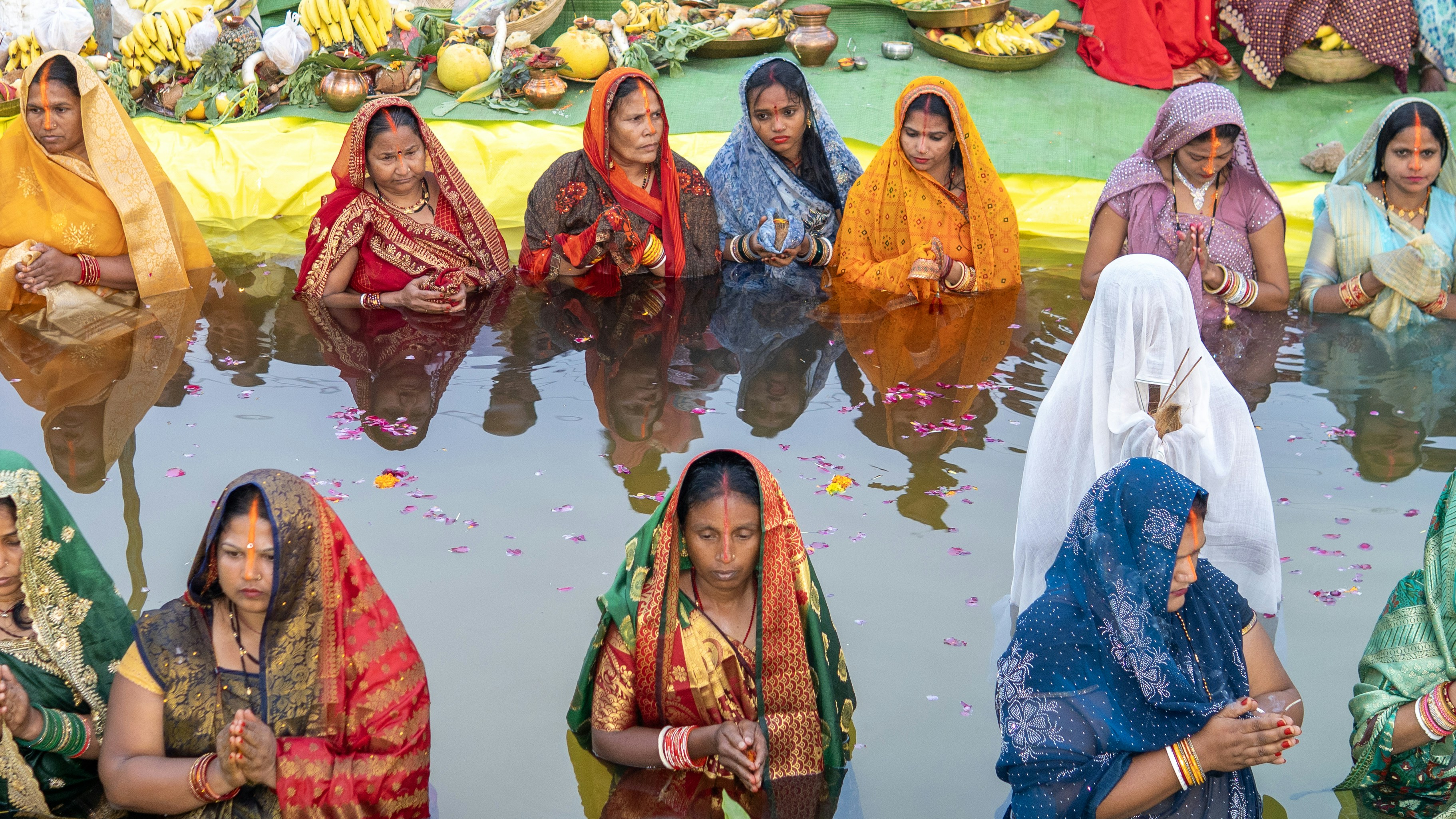Devotees offering prayers during Chhath Puja, a traditional Hindu festival dedicated to the Sun God. | Women praying in a body of water
