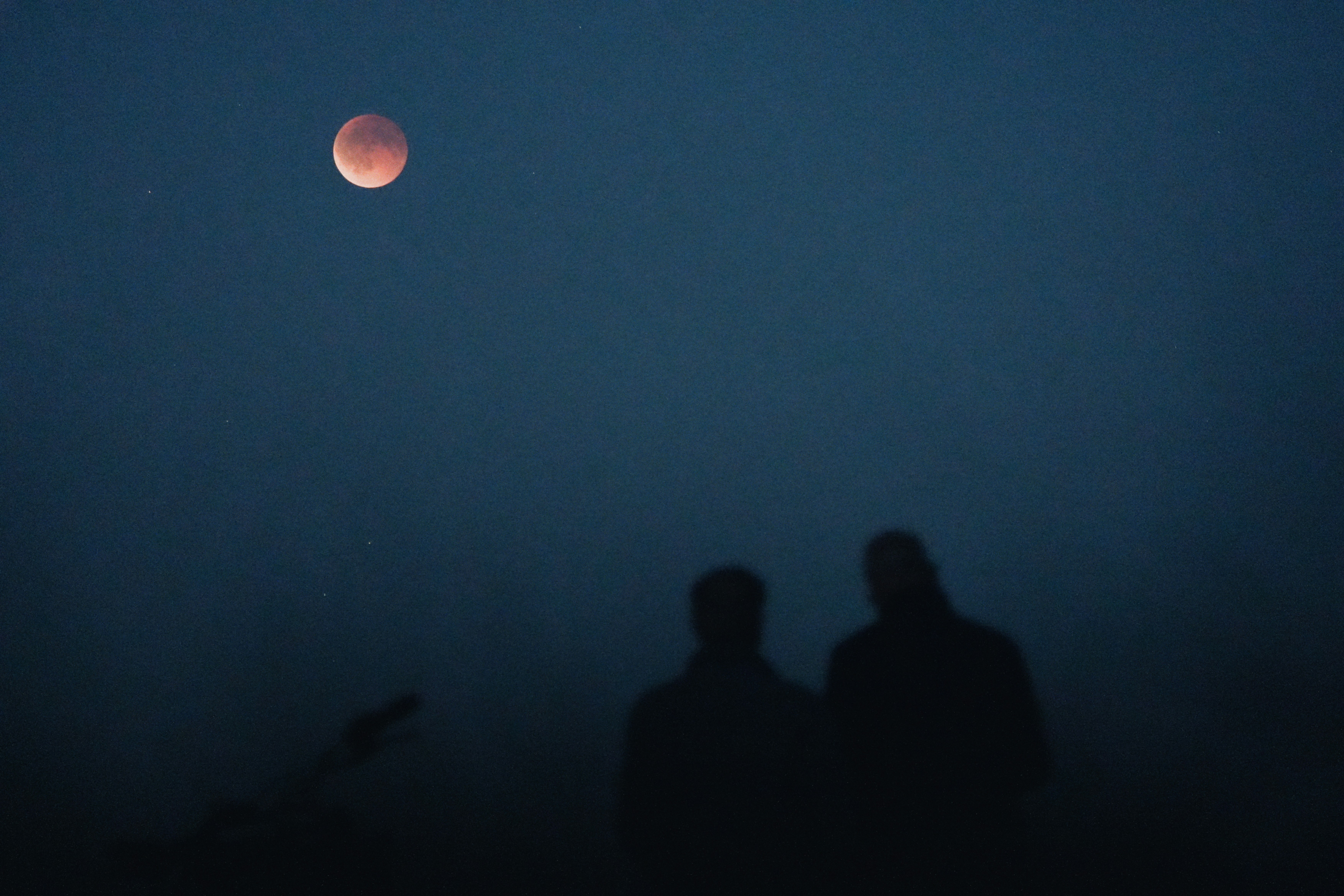 Two people watch a lunar eclipse in the night sky