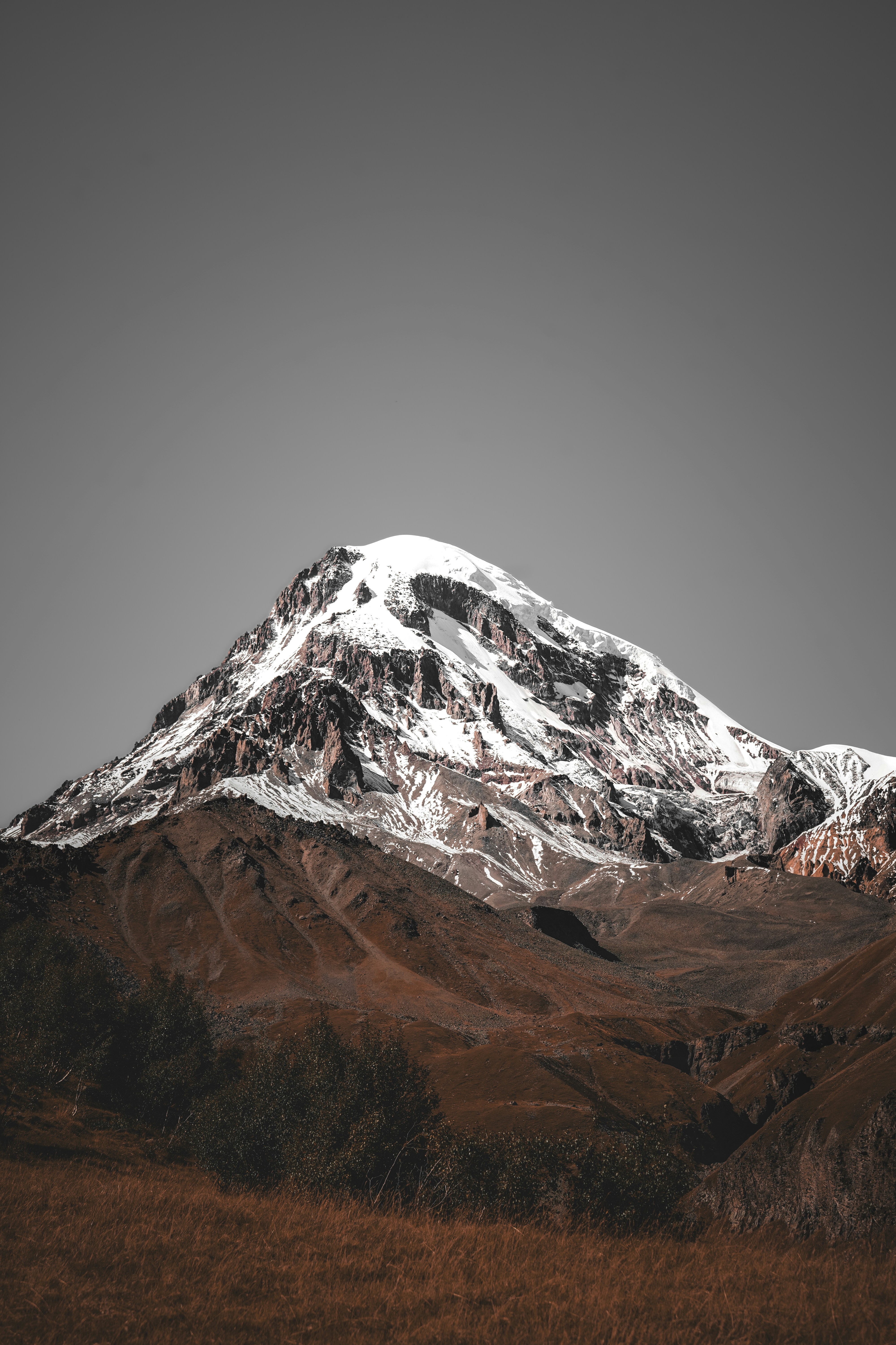 Snow-capped mountain rises above rugged terrain, showcasing the stark contrast of winter against the earthy landscape. A tranquil scene of nature's grandeur.