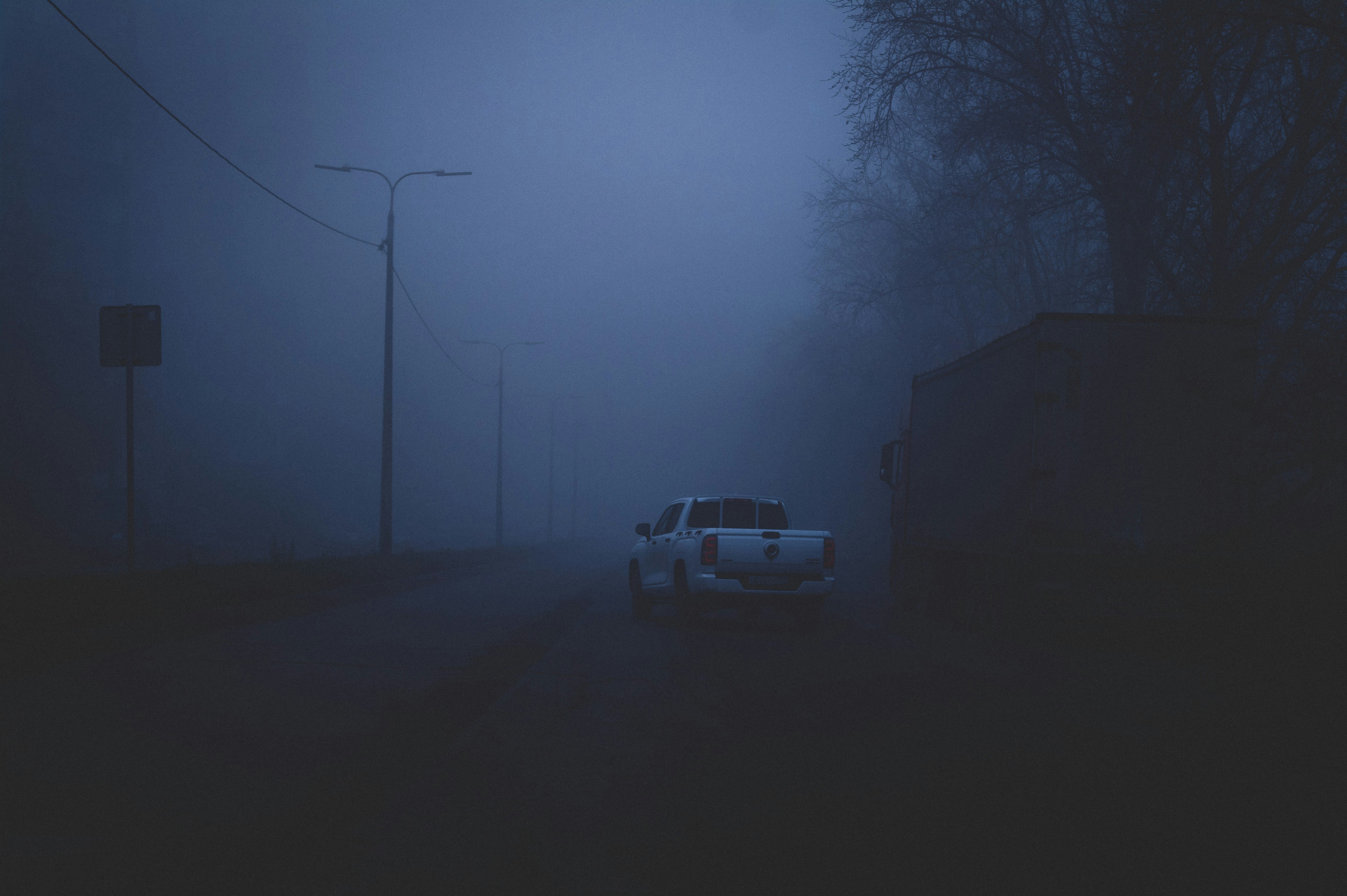 A lone white pickup truck parked on a deserted road enveloped in thick fog, creating an atmosphere of solitude and intrigue.