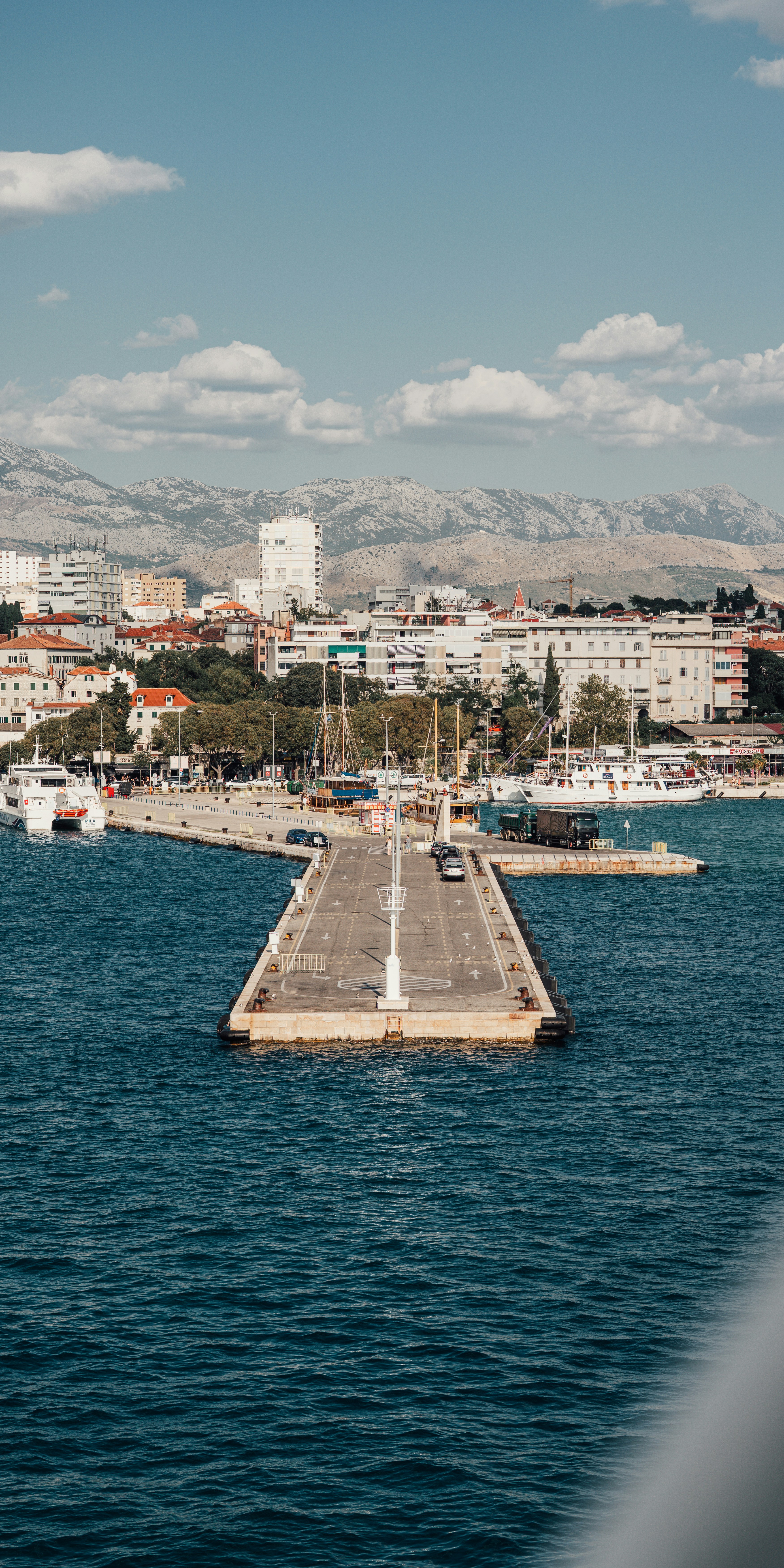 Pier extending into the blue ocean with city skyline.
