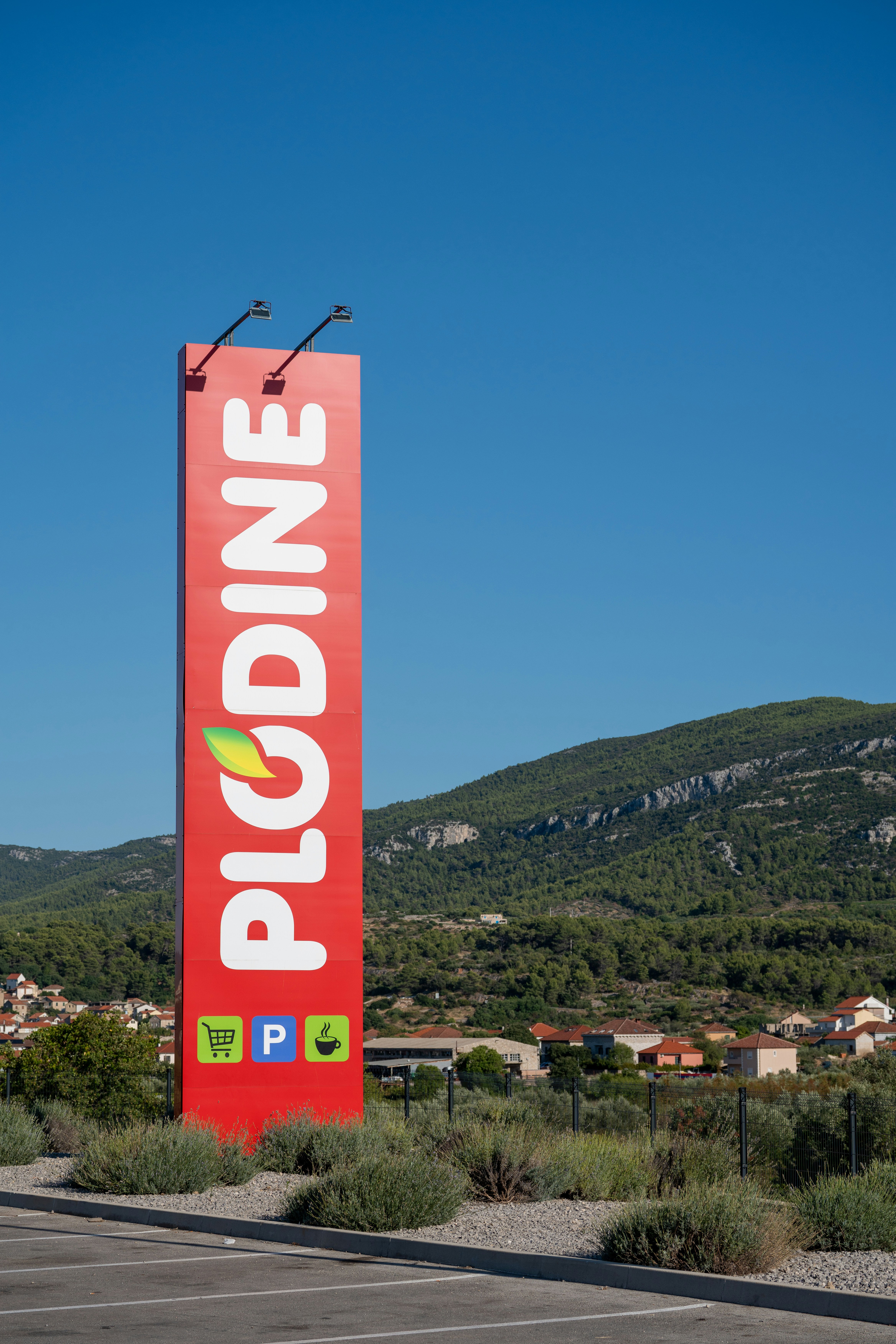 Crimson Tower: The PLODINE Sign Reaching into a Clear Blue Sky