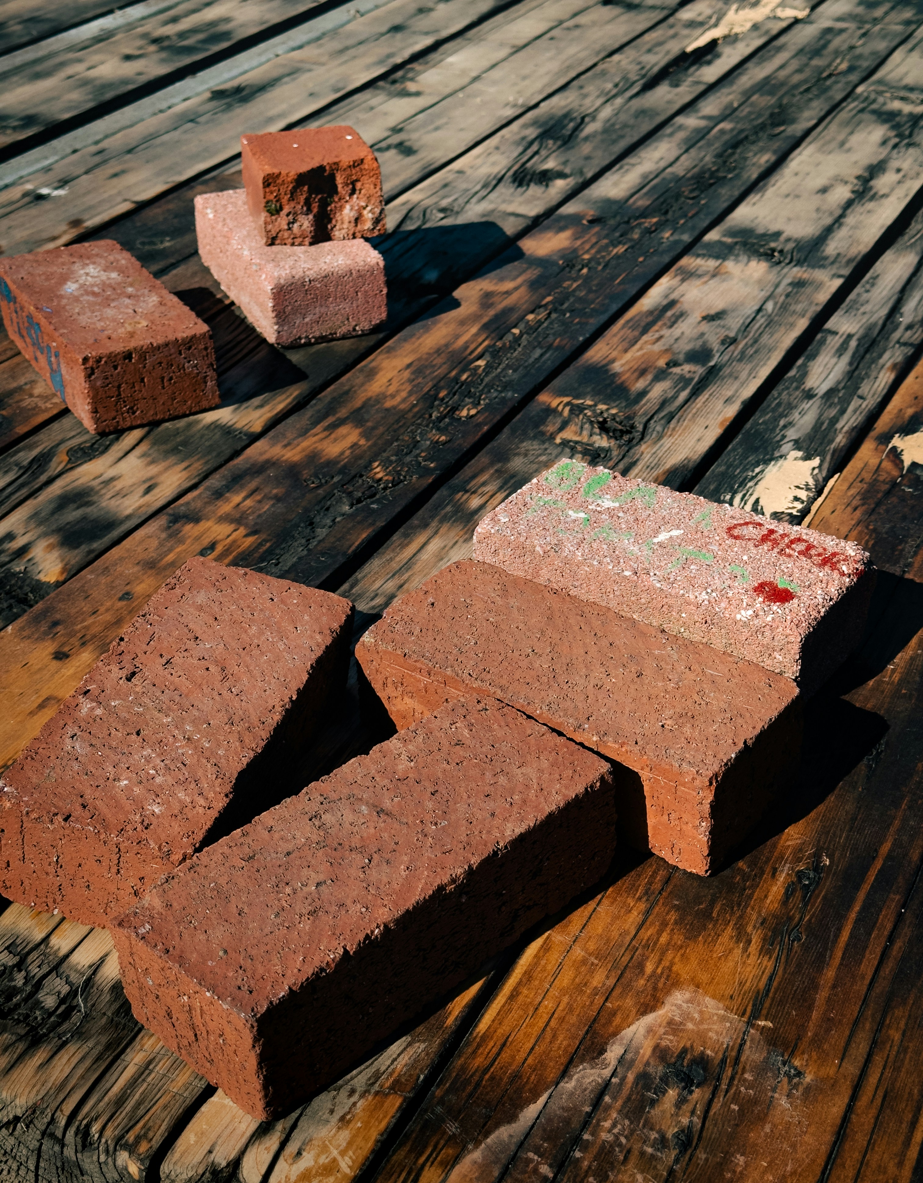 Some bricks on the wooden table. | Red bricks scattered on a weathered wooden surface.