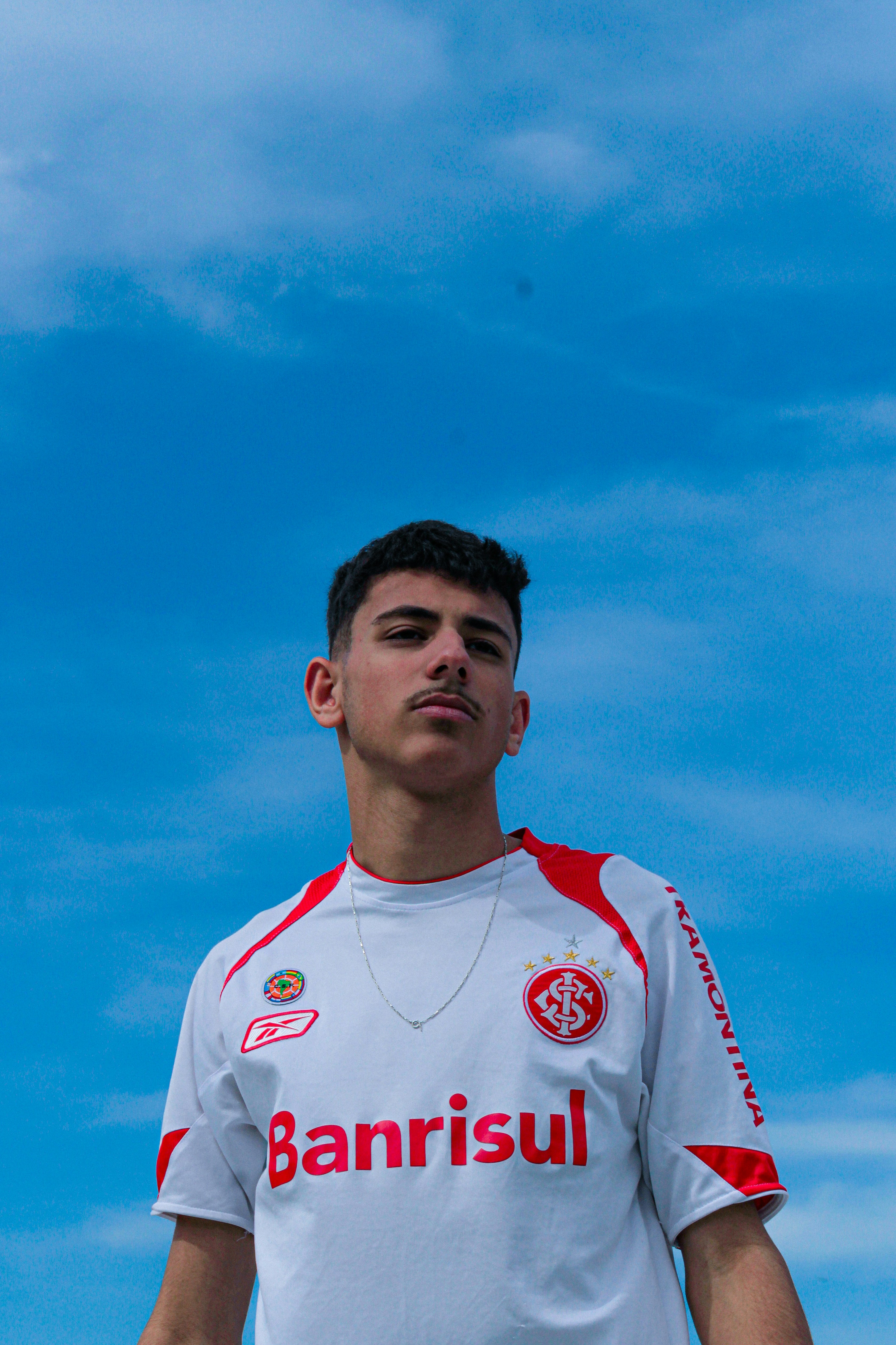 Young man in a sports jersey stands confidently against a blue sky, embodying determination and athleticism.