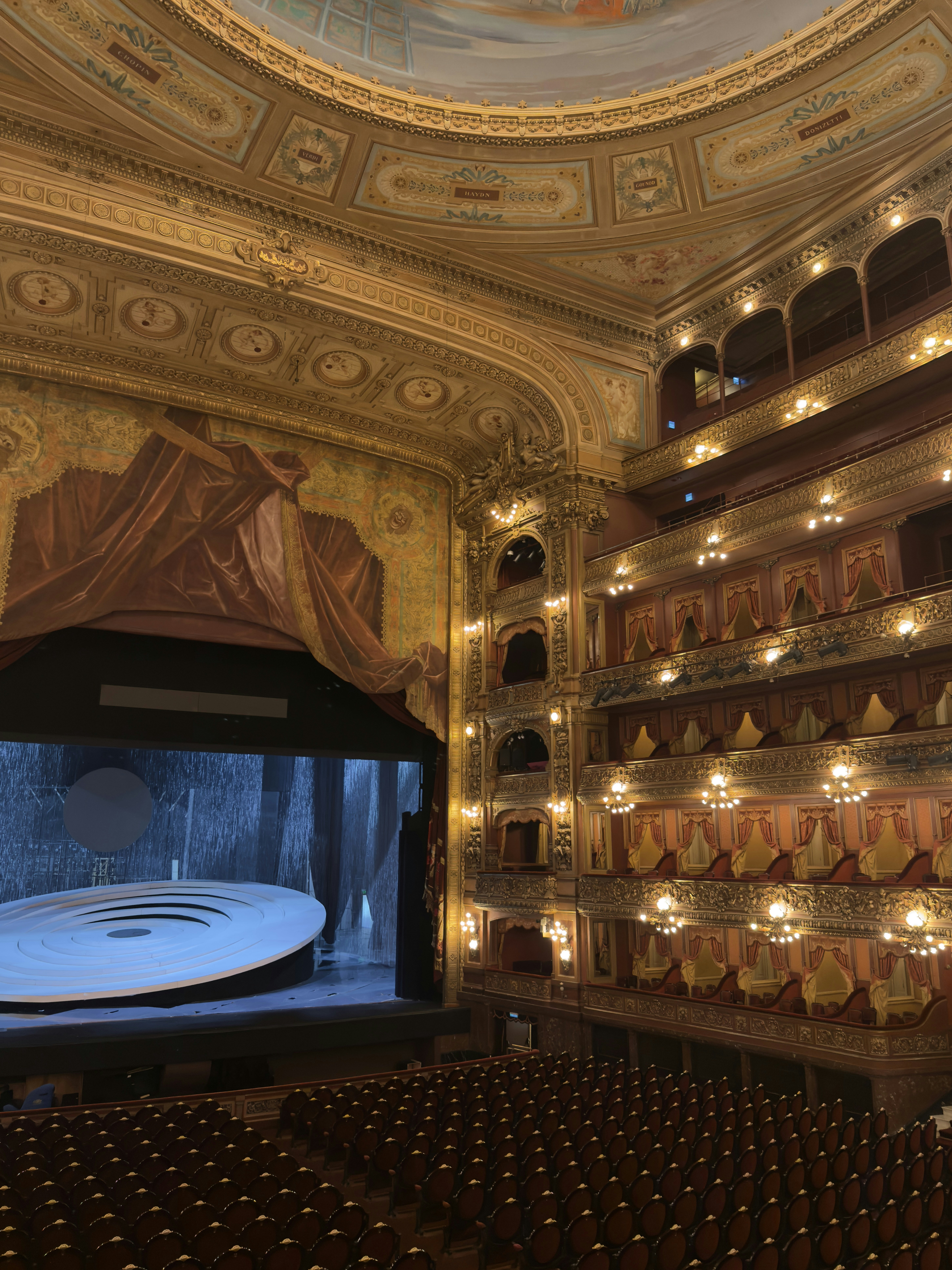 Intricate interior of a historic theater showcasing a lavish stage adorned with a grand curtain and an elaborate ceiling mural.