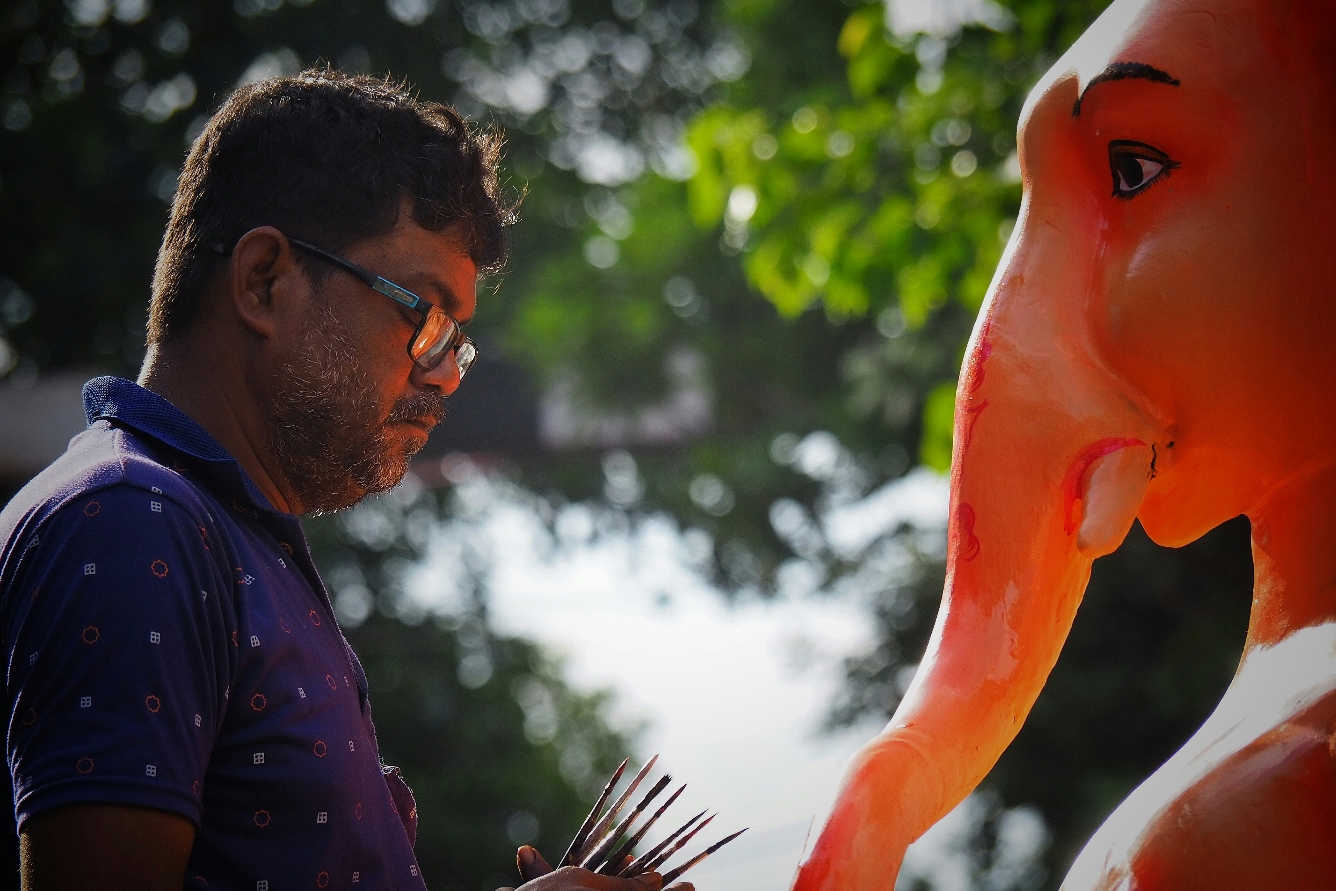 Man painting an orange ganesha idol with brushes