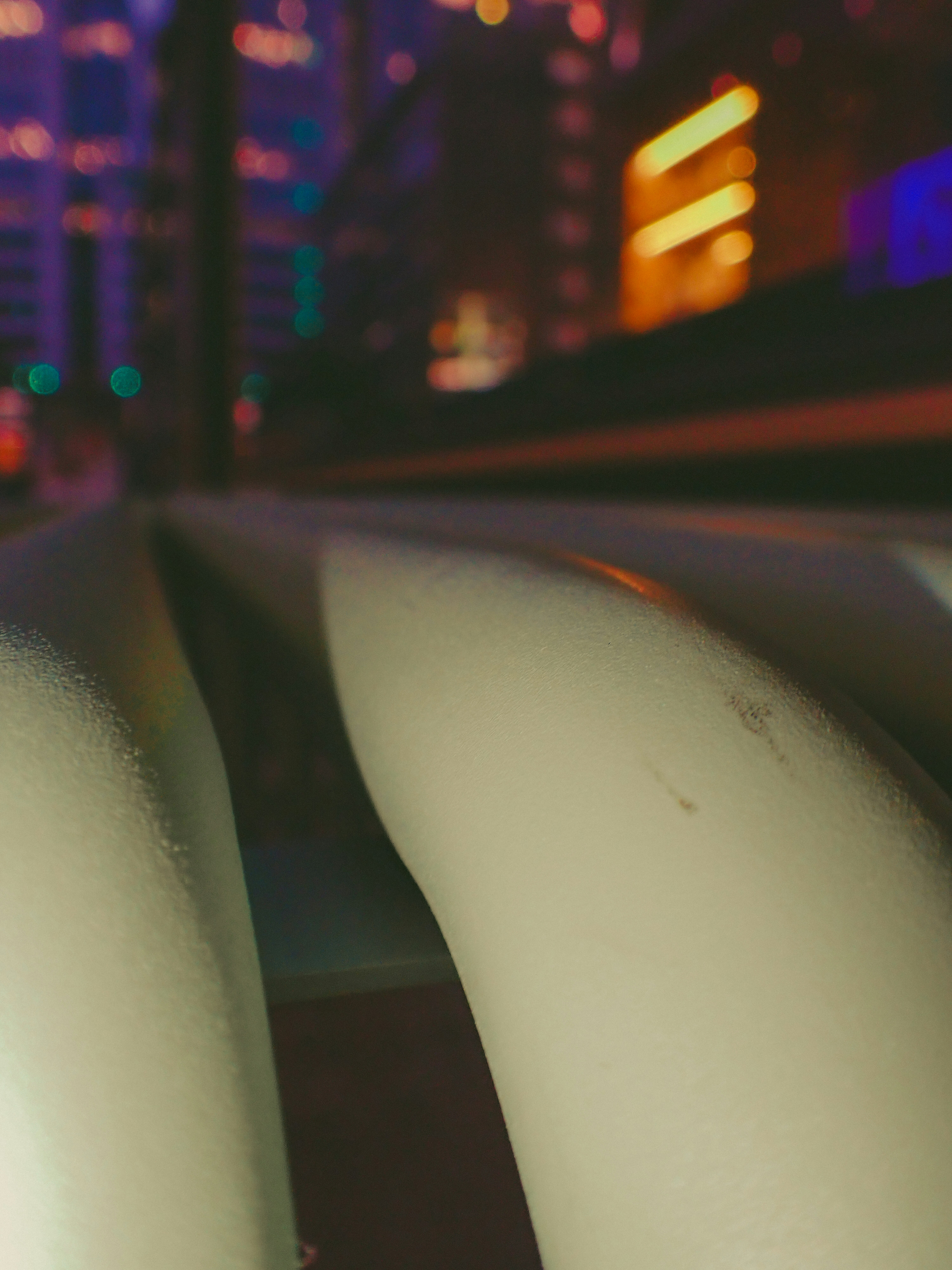 Close-up of curved railings reflecting vibrant city lights at night. The interplay of colors creates a dynamic urban atmosphere.