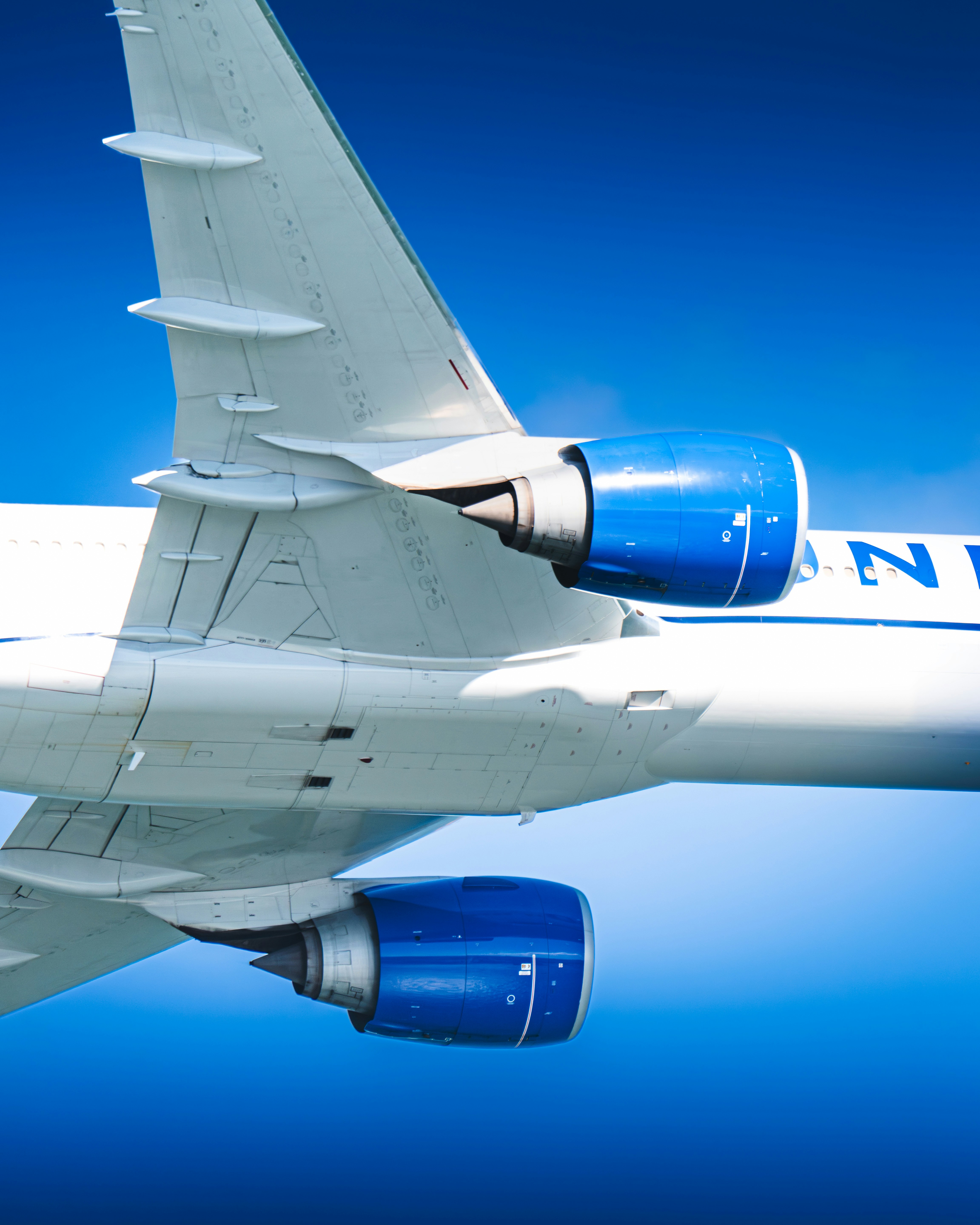 Close-up of an airplane's wing and engine against a vibrant blue sky. The design highlights the engineering marvel of modern aviation.