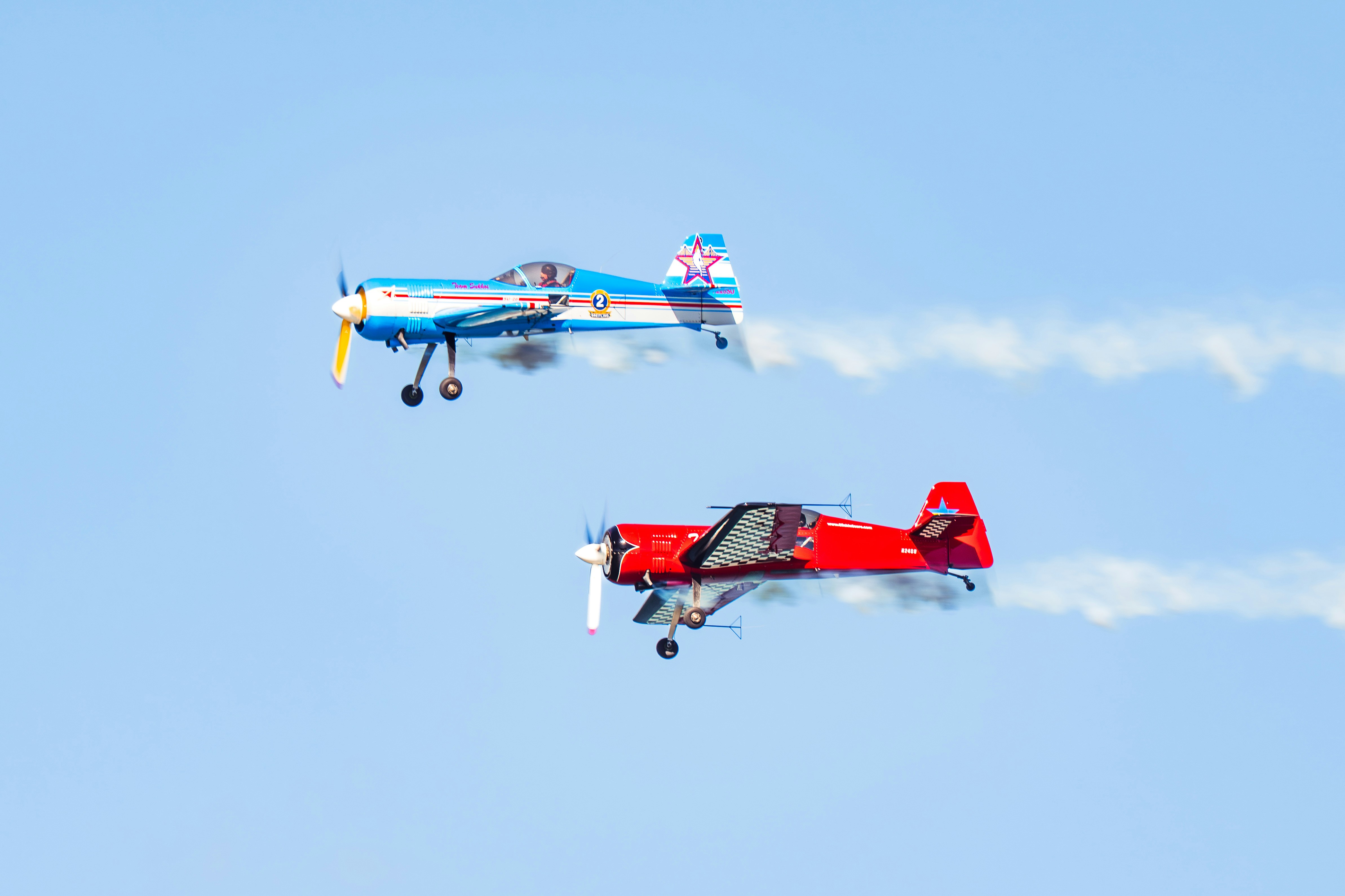 Two aerobatic planes performing synchronized maneuvers against a clear blue sky.