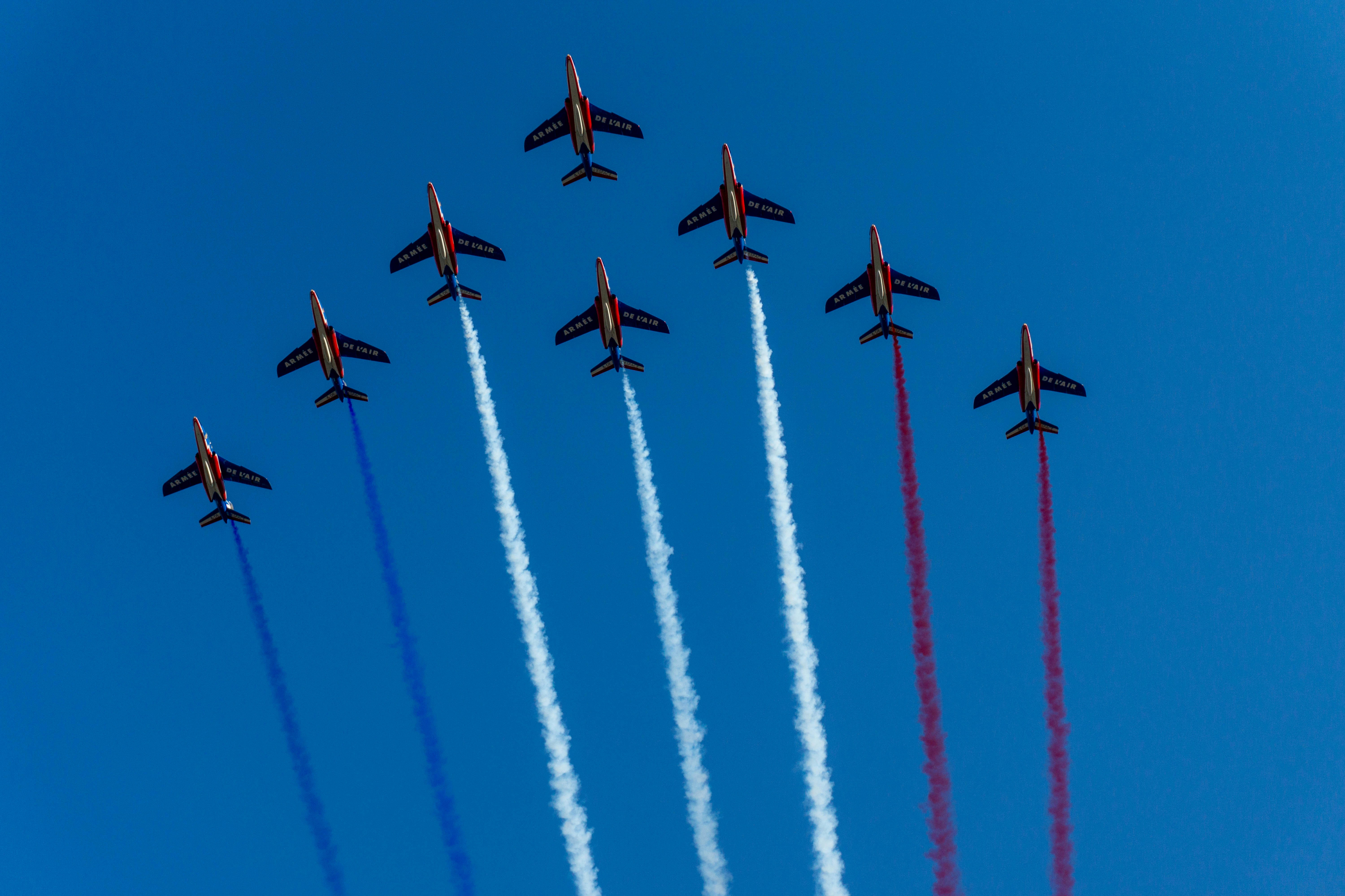 Nine fighter jets fly in formation leaving colored smoke trails.