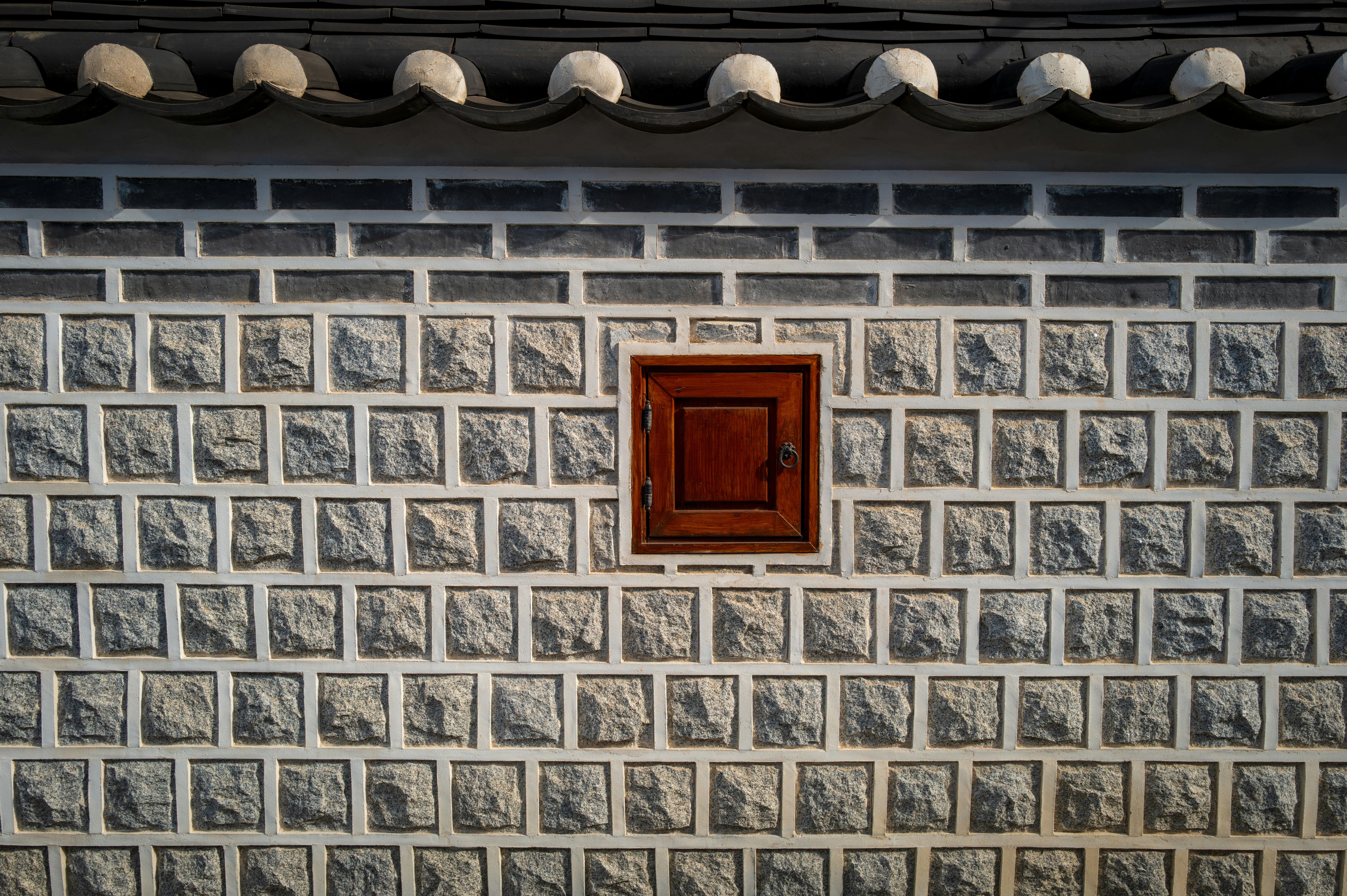 The Quiet Hatch: A Wooden Door Embedded in a Stone Grid