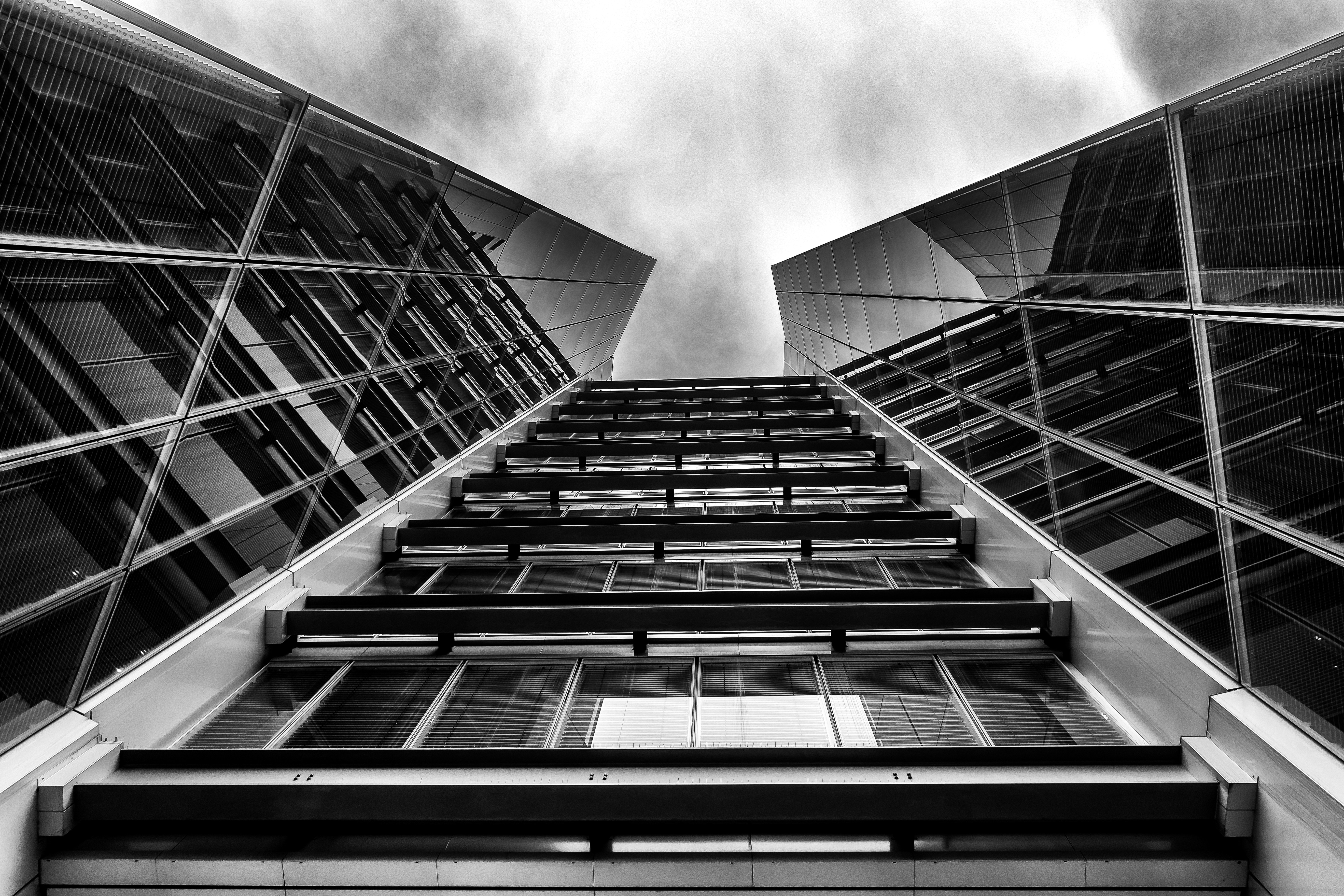 Modern architectural facade reflecting clouds above, emphasizing vertical lines and symmetry.