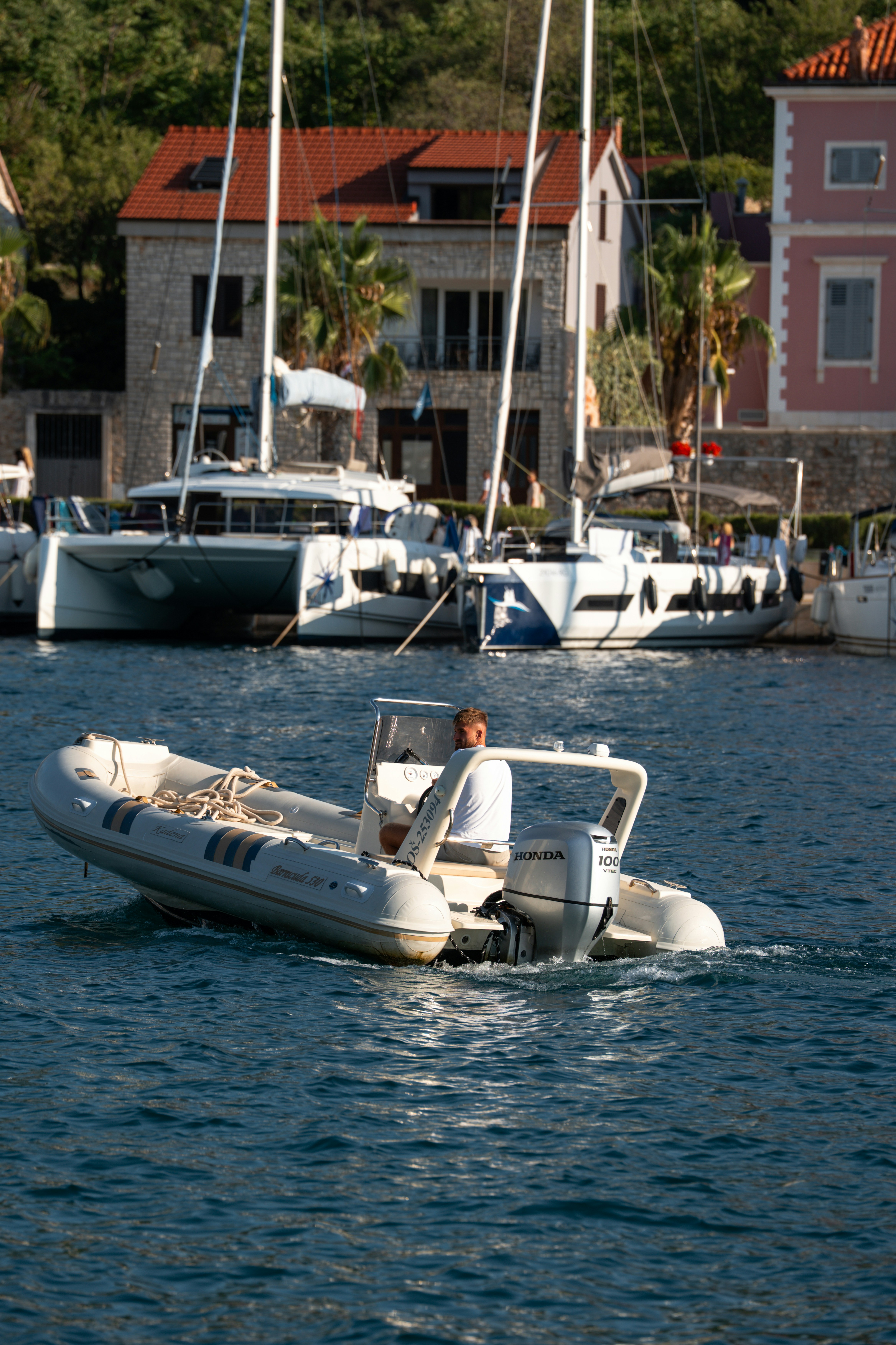 A small inflatable boat navigates through calm waters, surrounded by moored yachts and charming coastal architecture.