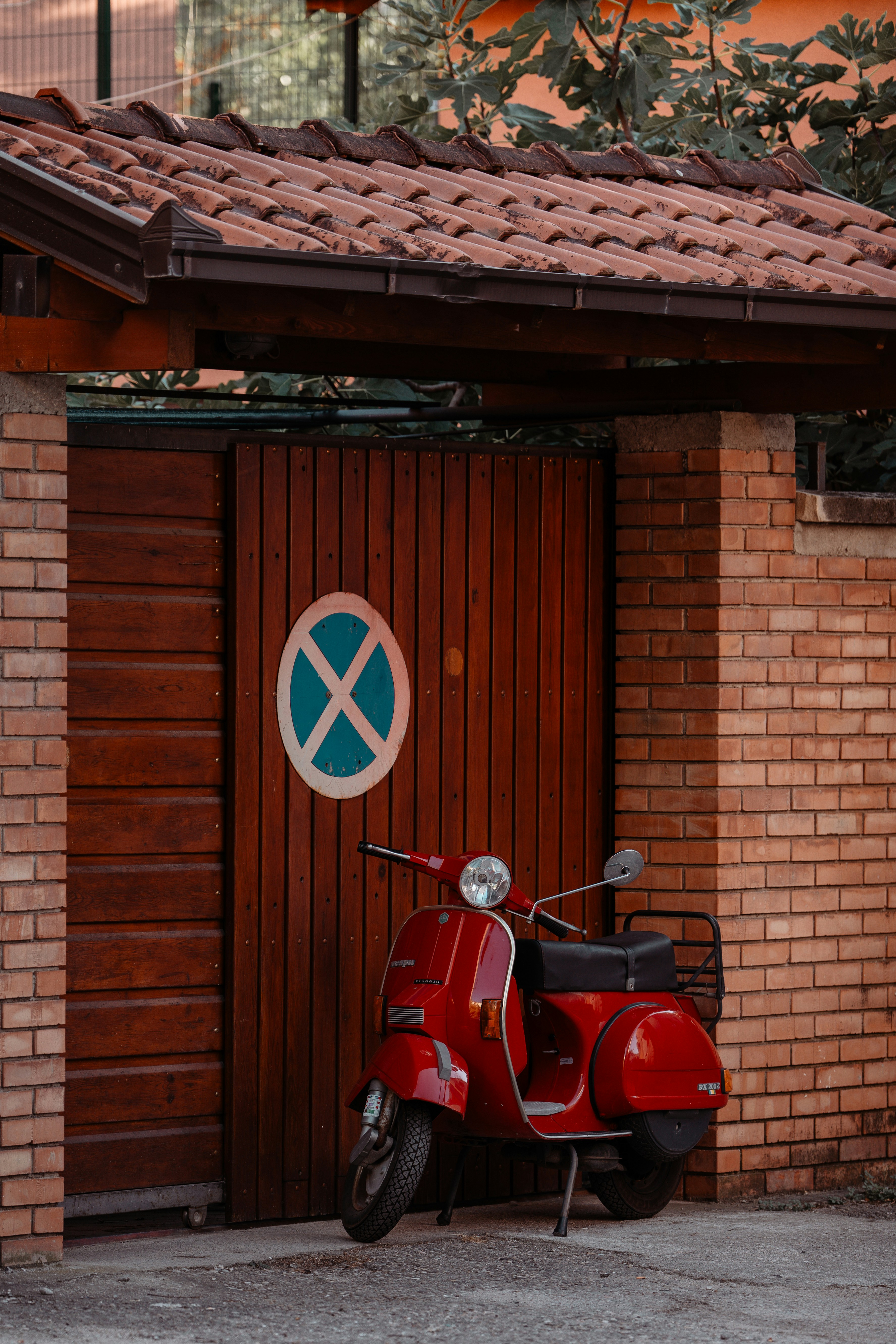 Crimson Vespa Resting by a Brick Gate Beneath a Tile Roof