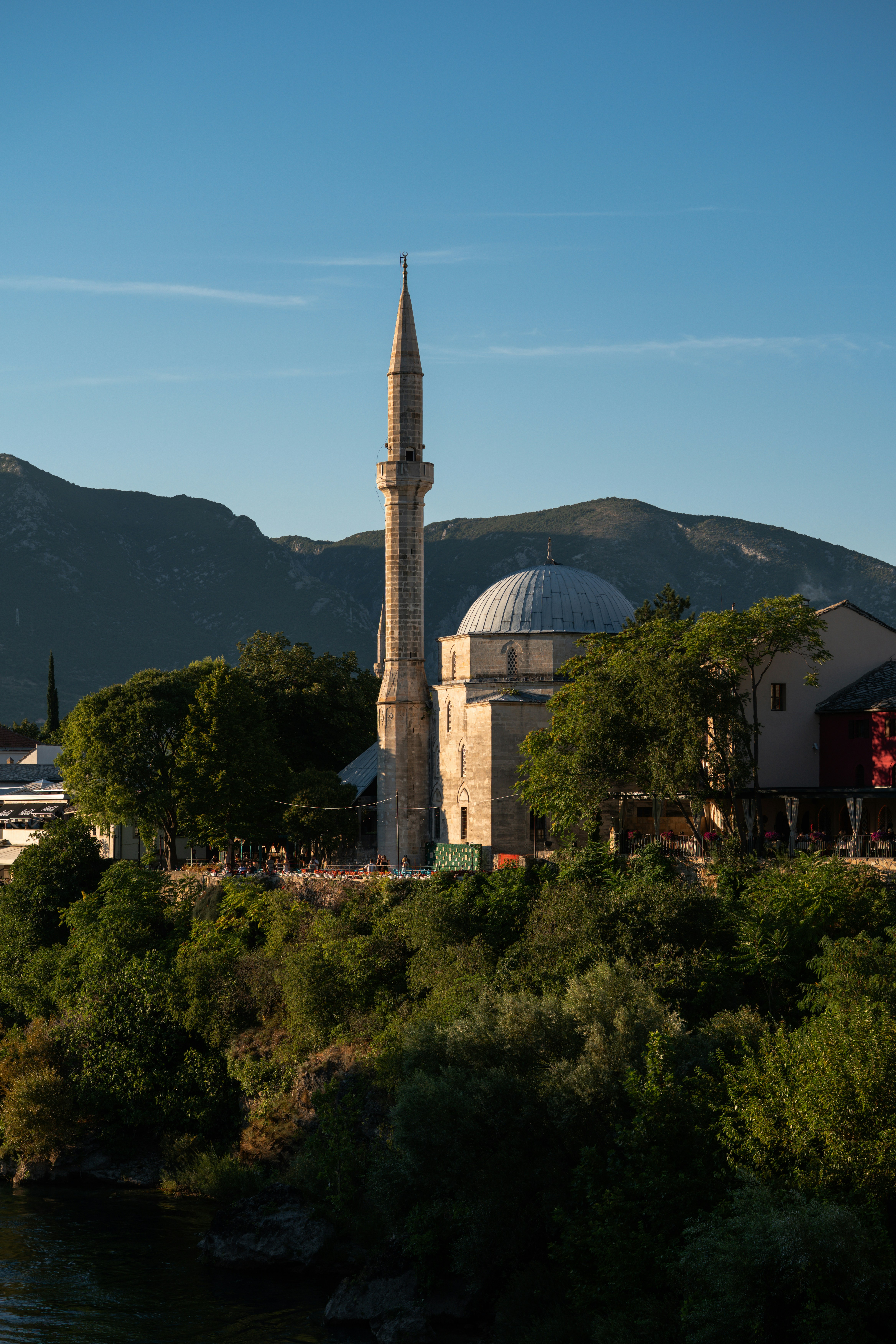 Minaret by the River: Stone Mosque Framed by Hills and Trees