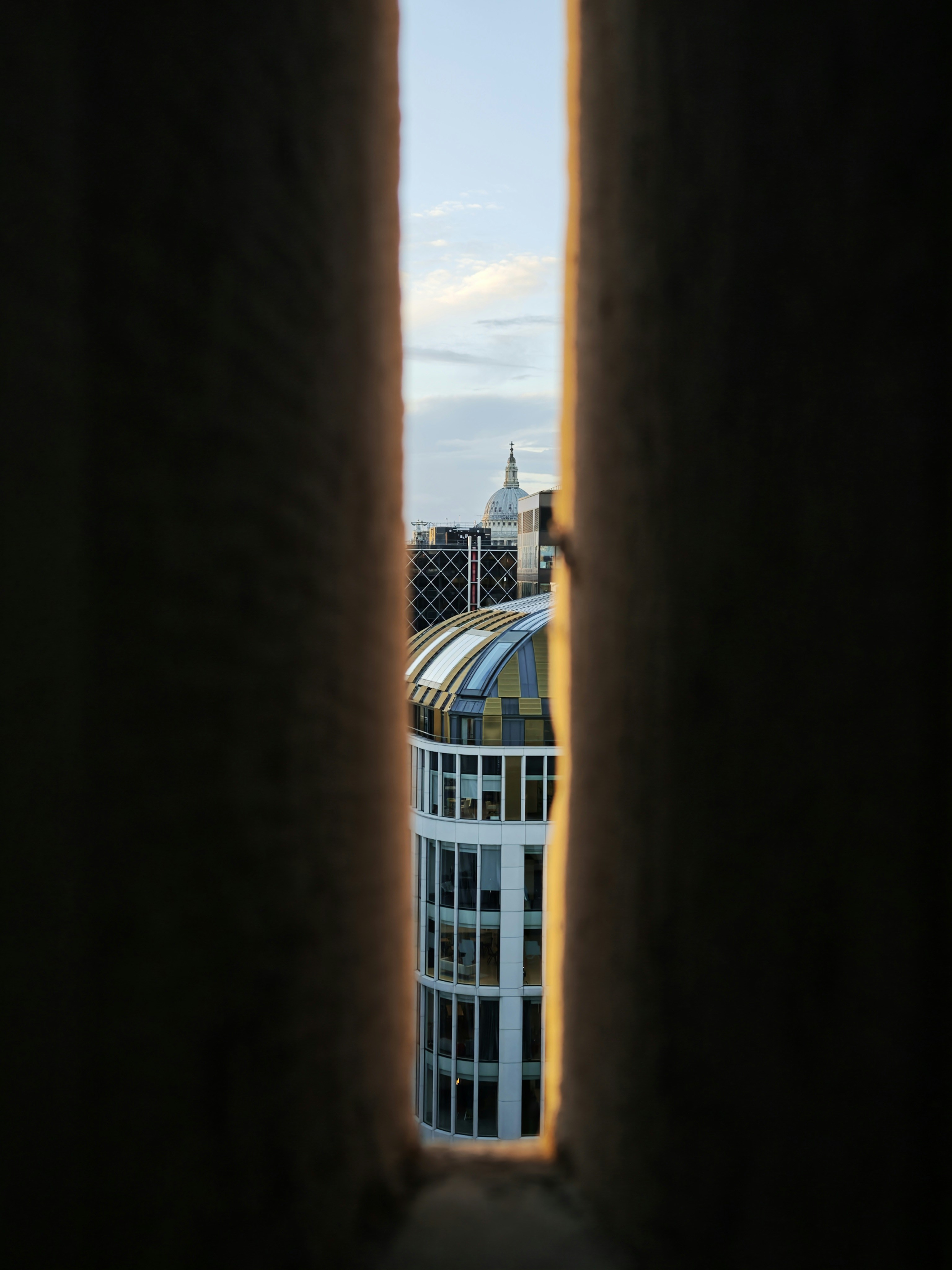 View of a city skyline framed by a narrow opening, showcasing a prominent dome structure and modern architecture. The scene captures the contrast between historical and contemporary design.