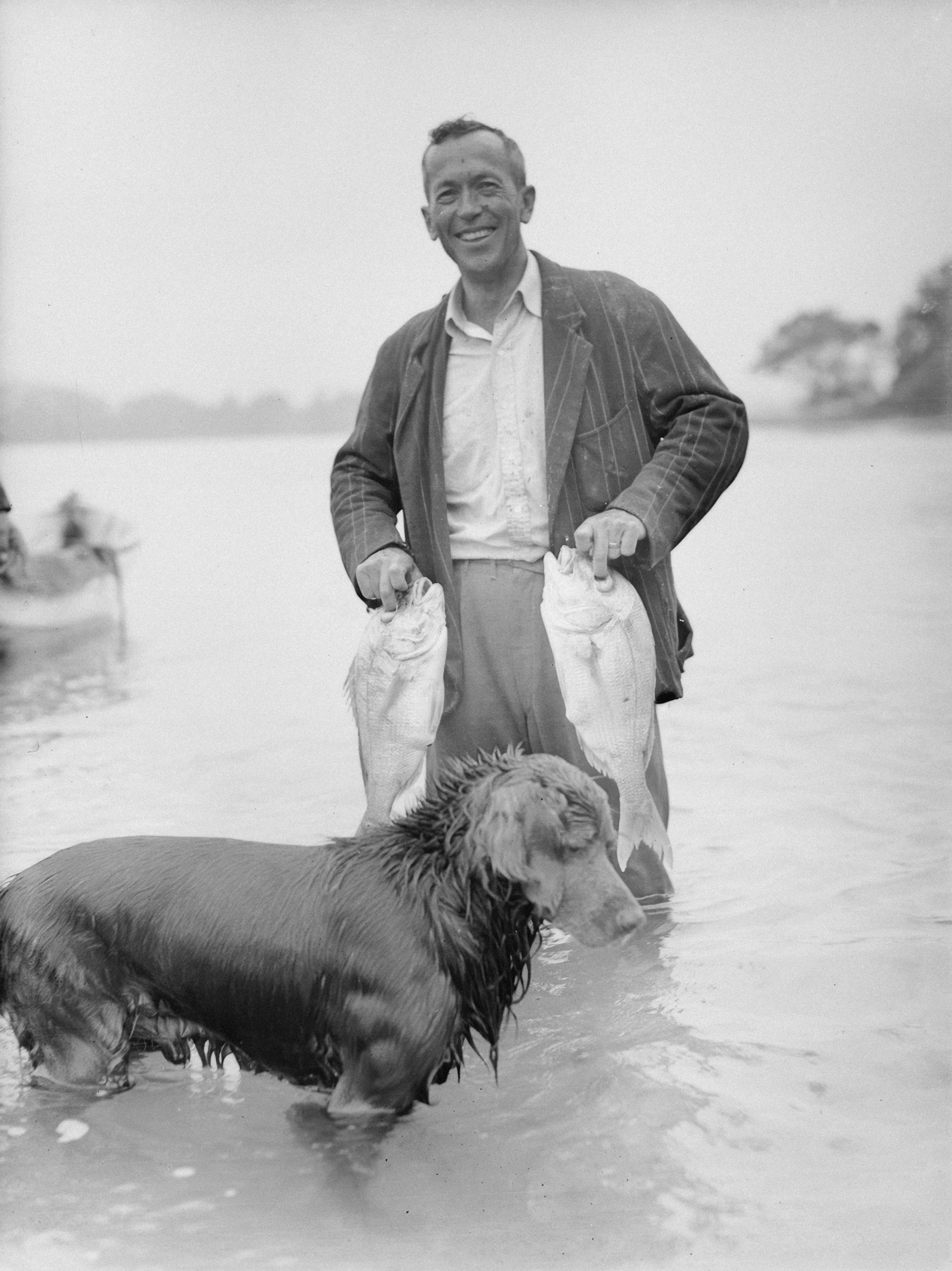 Two Fish, One Smile: A Riverbank Catch with a Wet-Furred Companion
