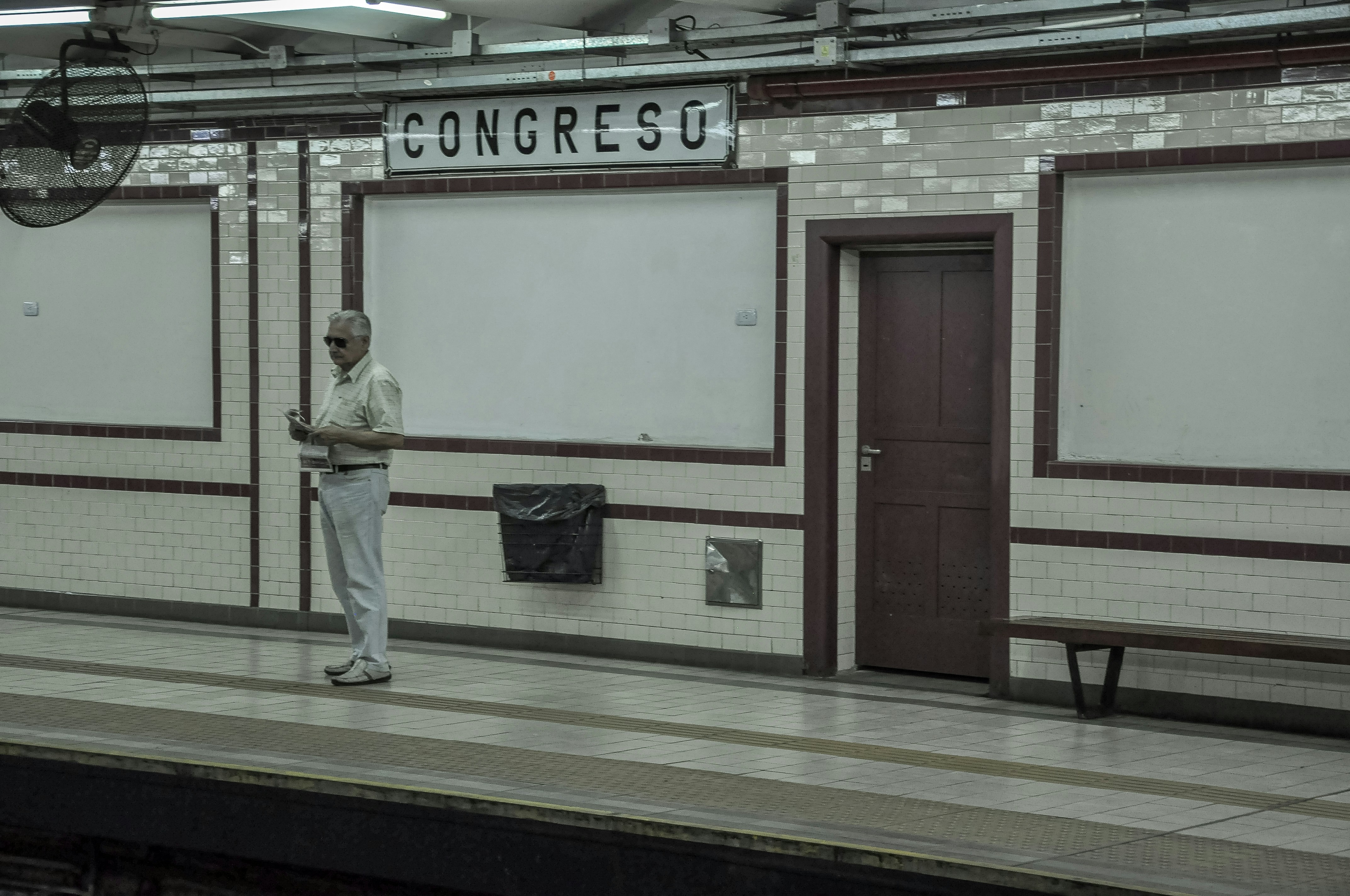 A lone figure stands on a subway platform under the sign 'Congreso,' surrounded by stark white tiles and minimalistic decor.