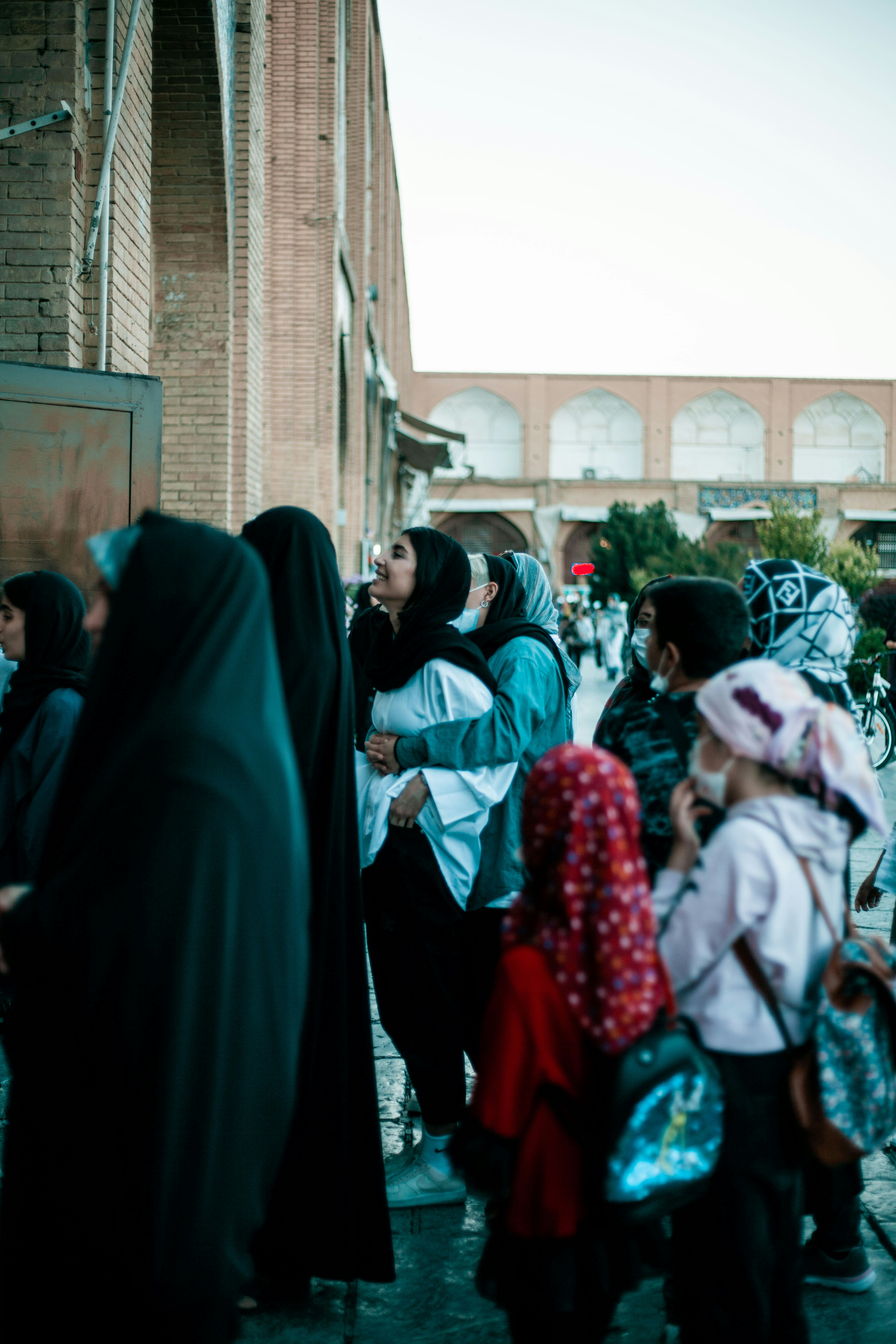 A diverse group of women and children, dressed in traditional attire, gazes intently at a display in an urban setting. The atmosphere is filled with anticipation.