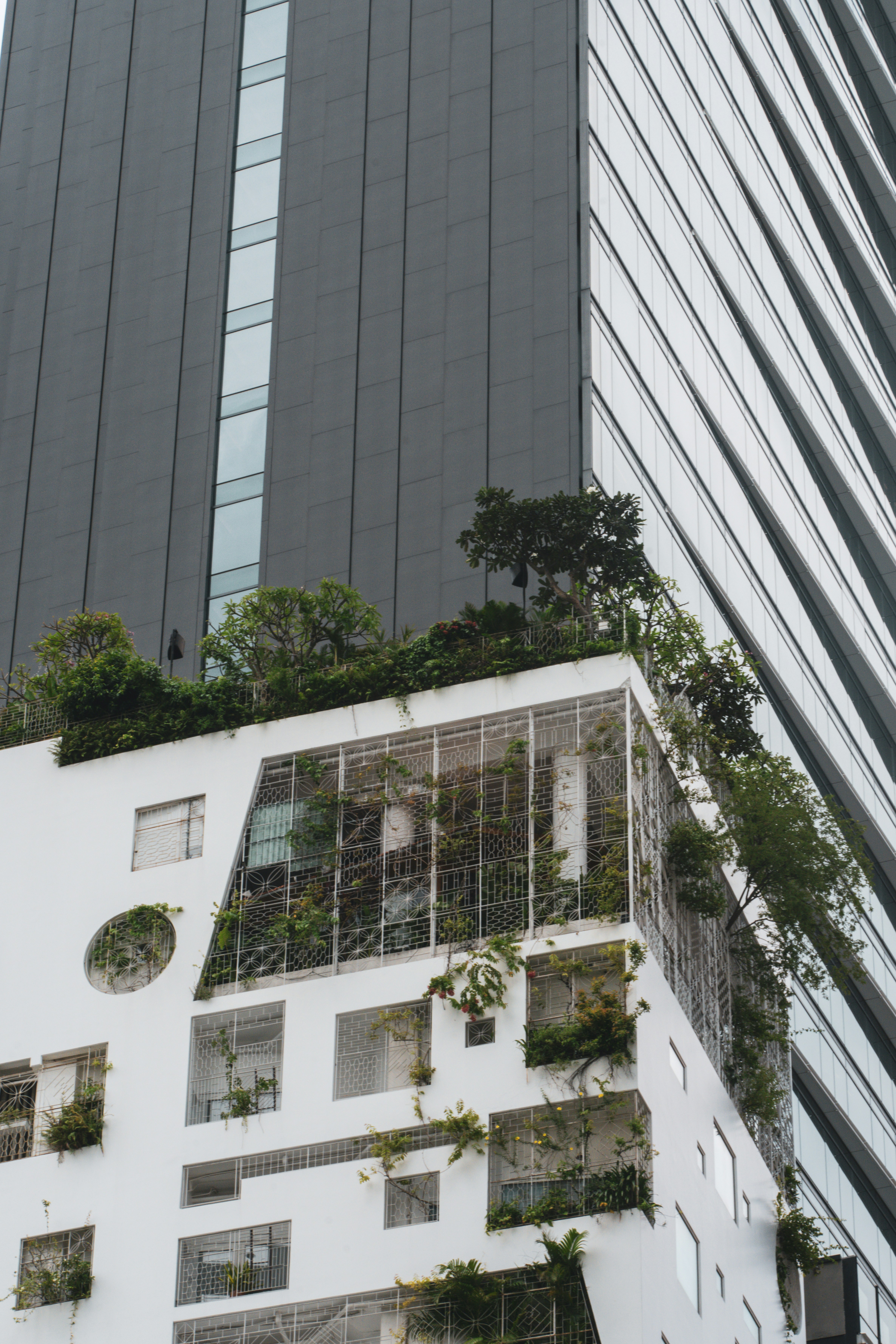 A unique architectural structure featuring lush greenery integrated into its design, contrasting with the sleek, modern skyscraper behind it.