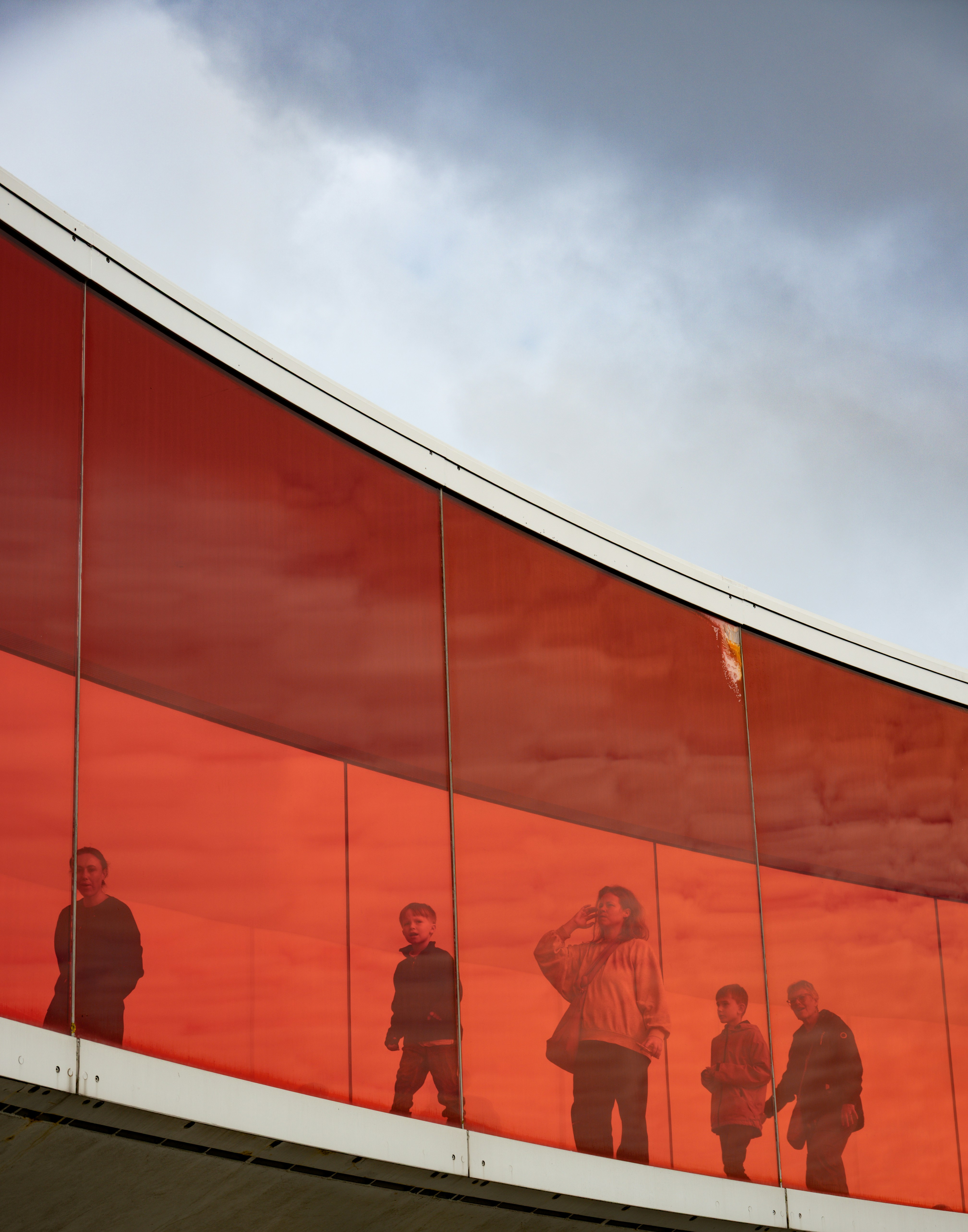 Echoes on a Red Curve: Passersby Silhouetted in Glass