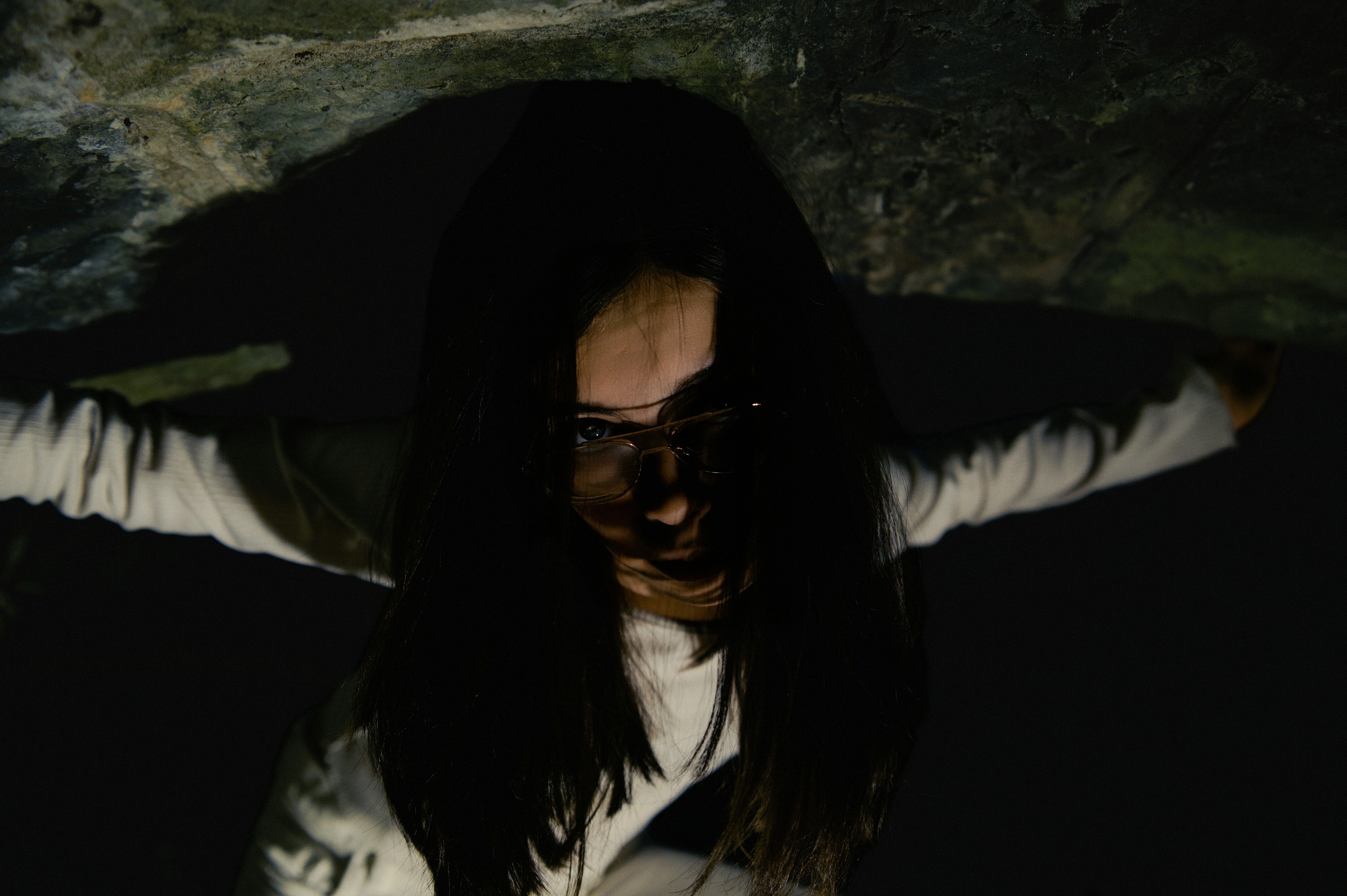 A figure with glasses emerges from the darkness, framed by jagged rock formations. The low light creates an eerie atmosphere, enhancing the sense of mystery.