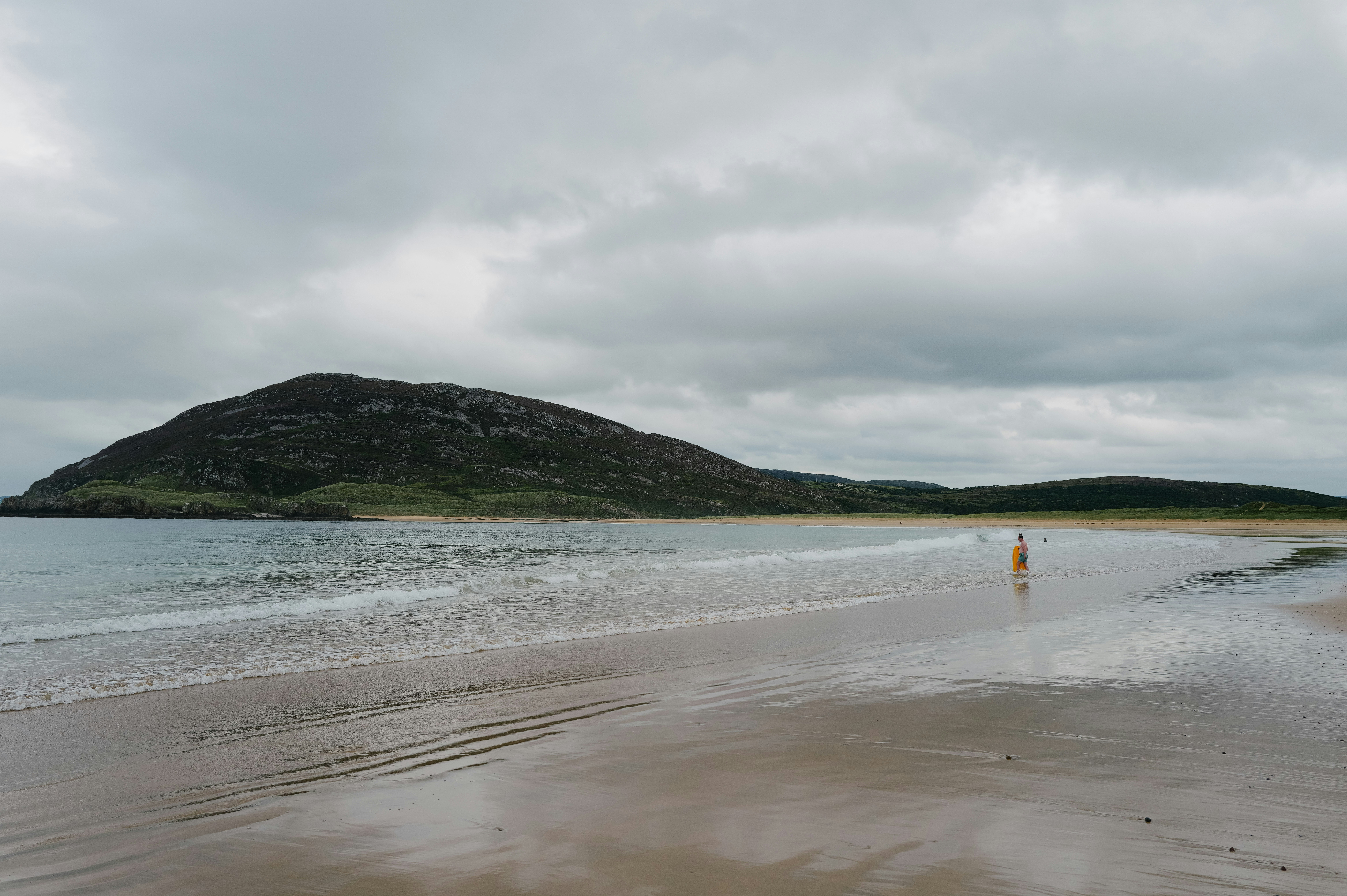 Person walks on a sandy beach with a large hill. photo – Free Beach ...