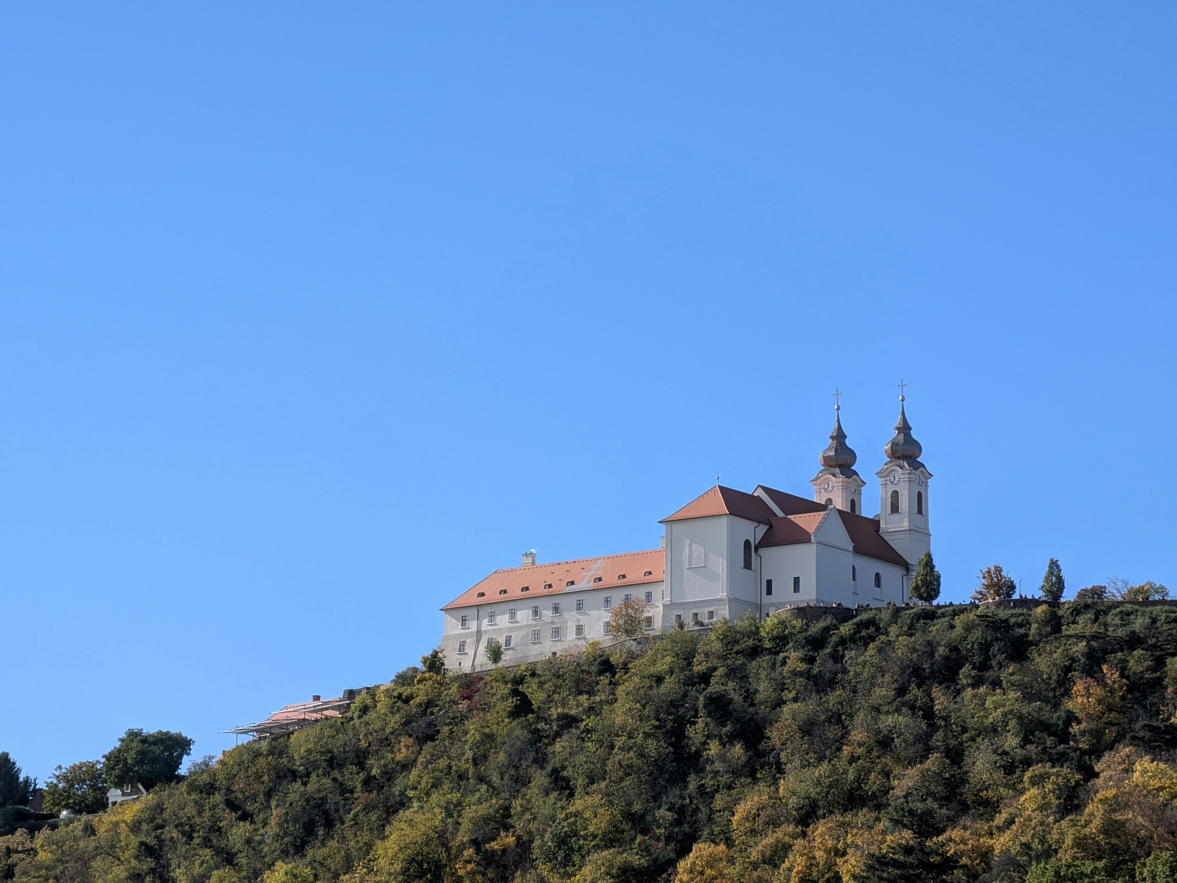 Historic church perched atop a verdant hill, framed by a clear blue sky.