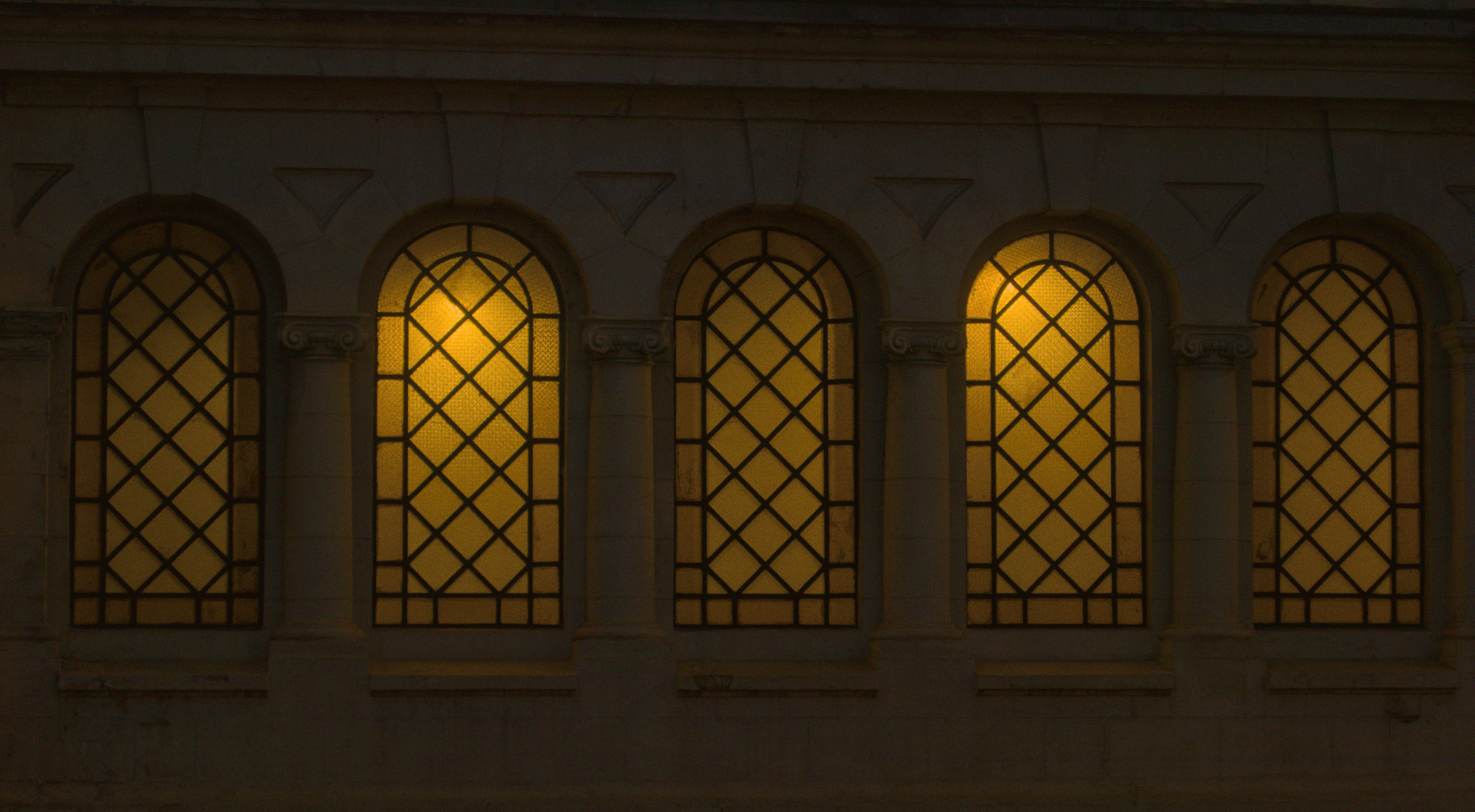 Five arched windows glowing with warm light at night.