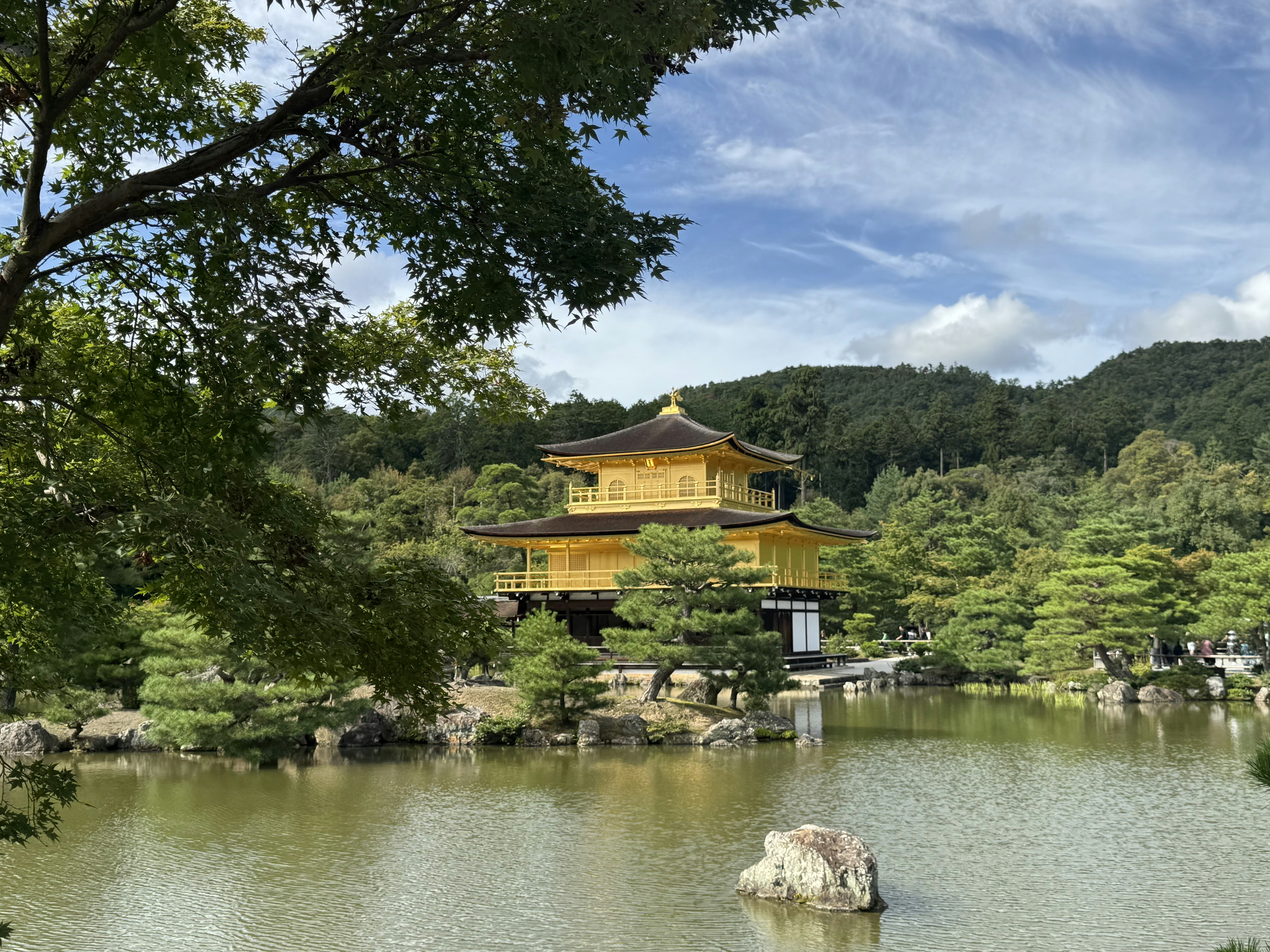 Golden temple reflecting in tranquil waters, surrounded by lush greenery and rocky formations.