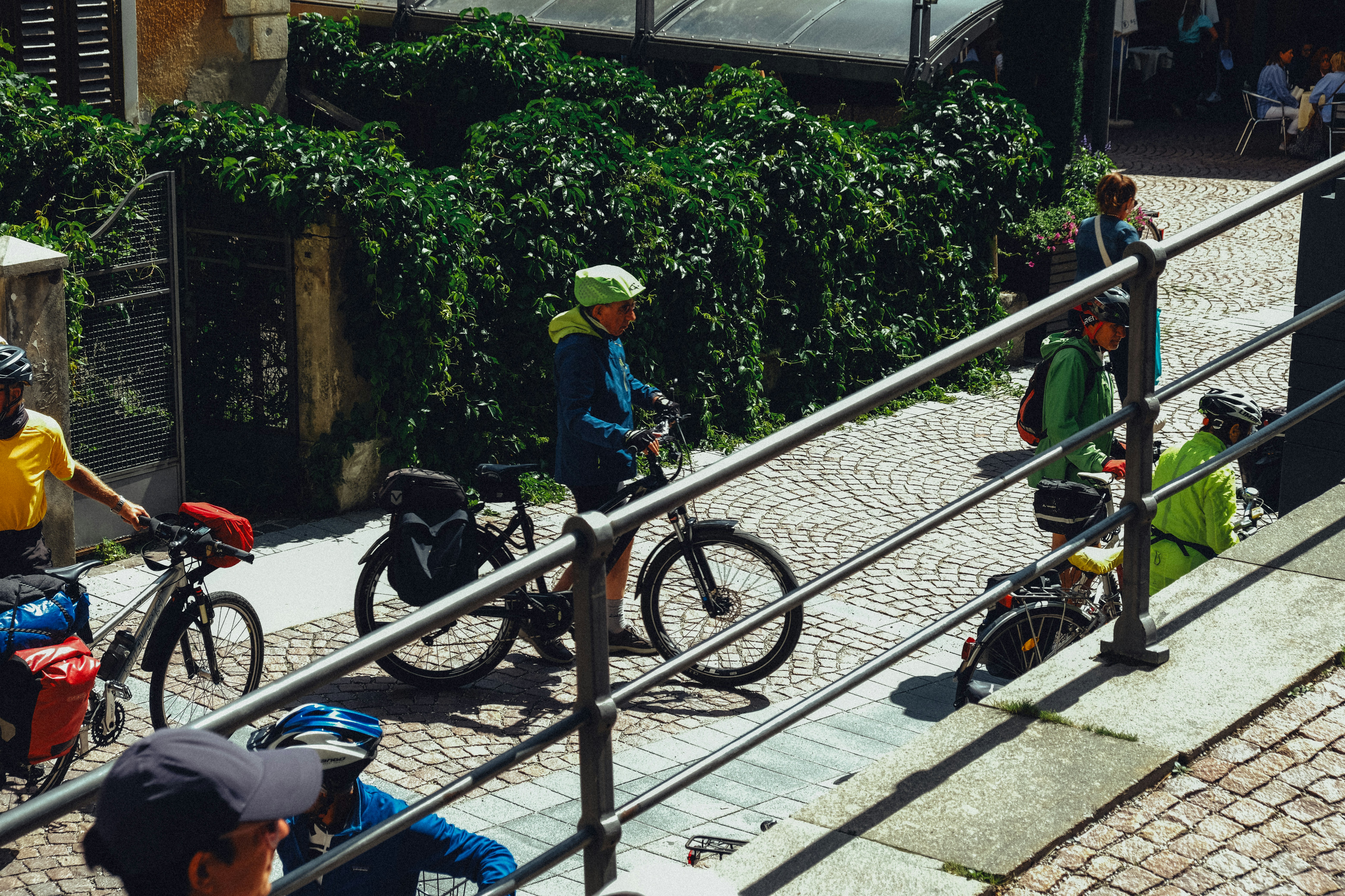Cyclists with loaded bikes on cobblestone street.