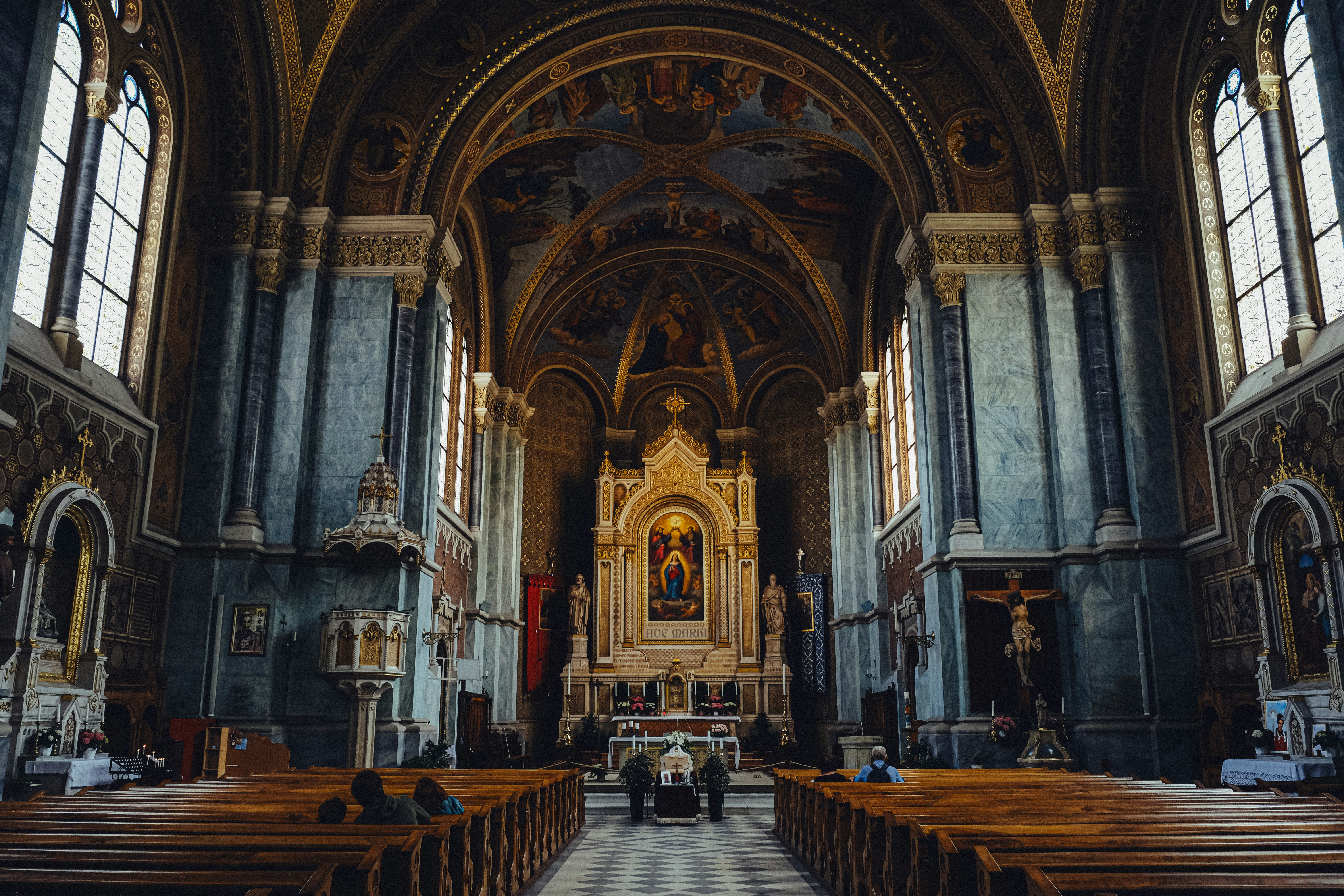 Interior of a grand church showcasing intricate architecture and serene atmosphere, with pews leading towards a beautifully adorned altar.