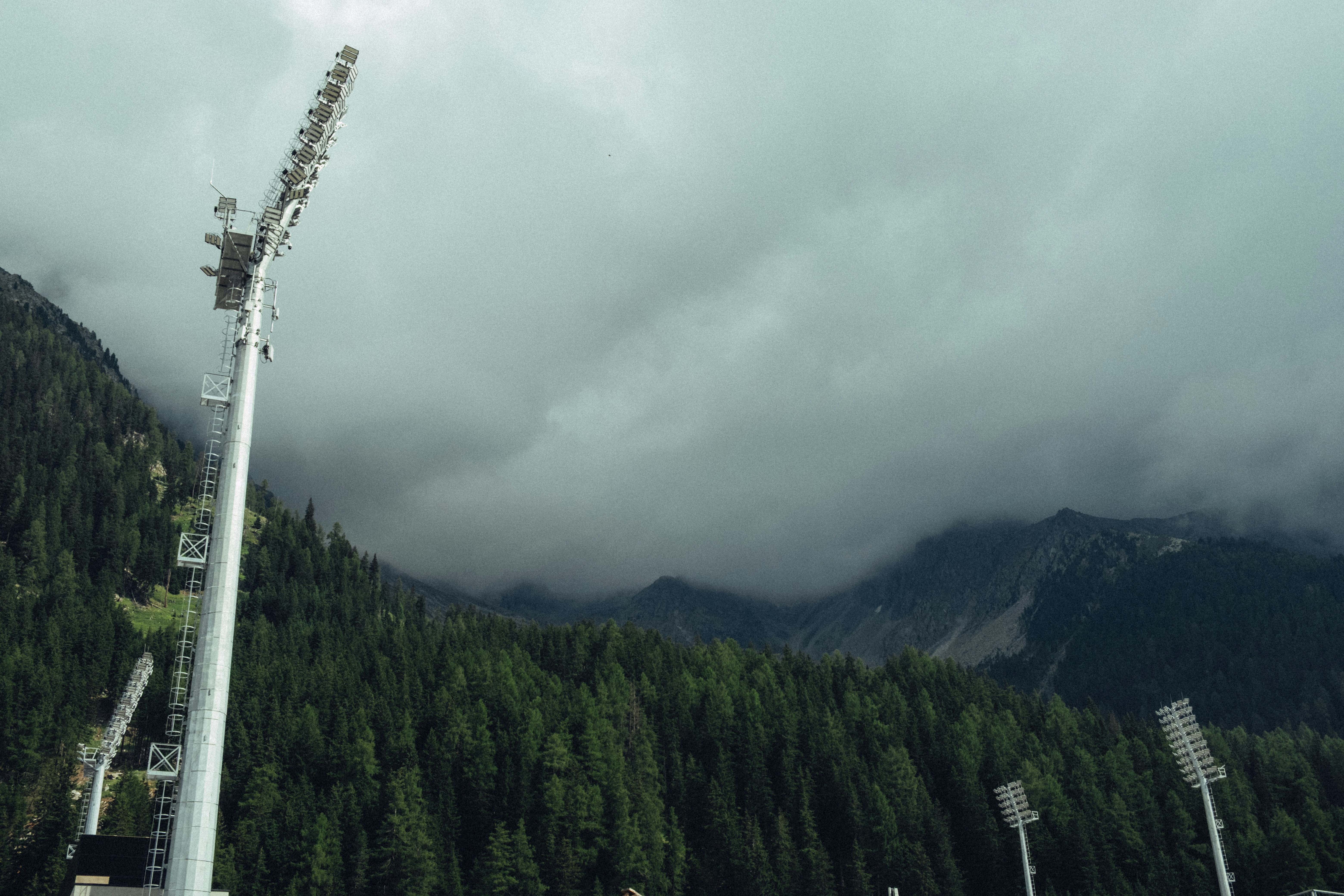 Tall floodlights stand against cloudy mountain forest backdrop