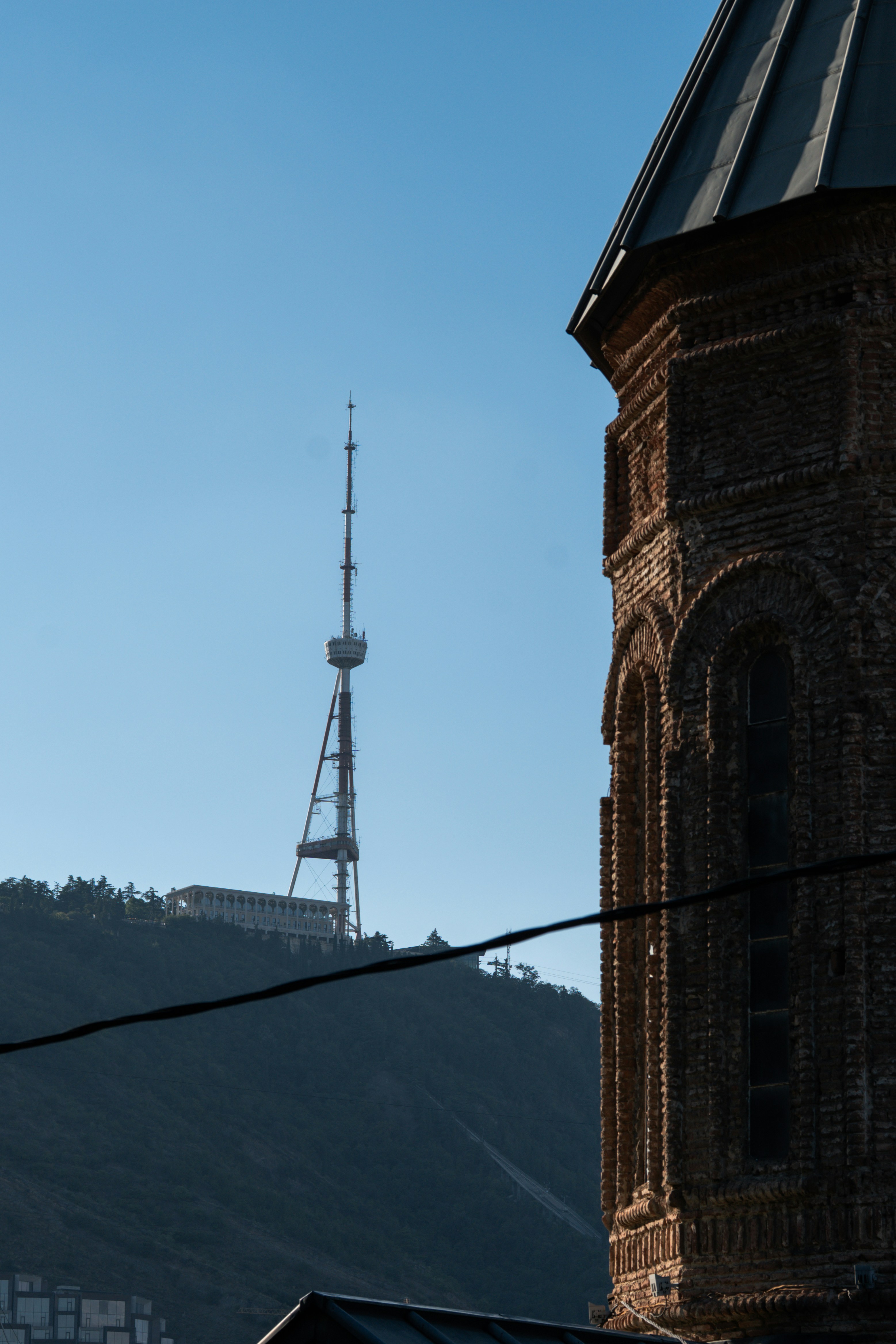 Television tower on a hill behind brick building.