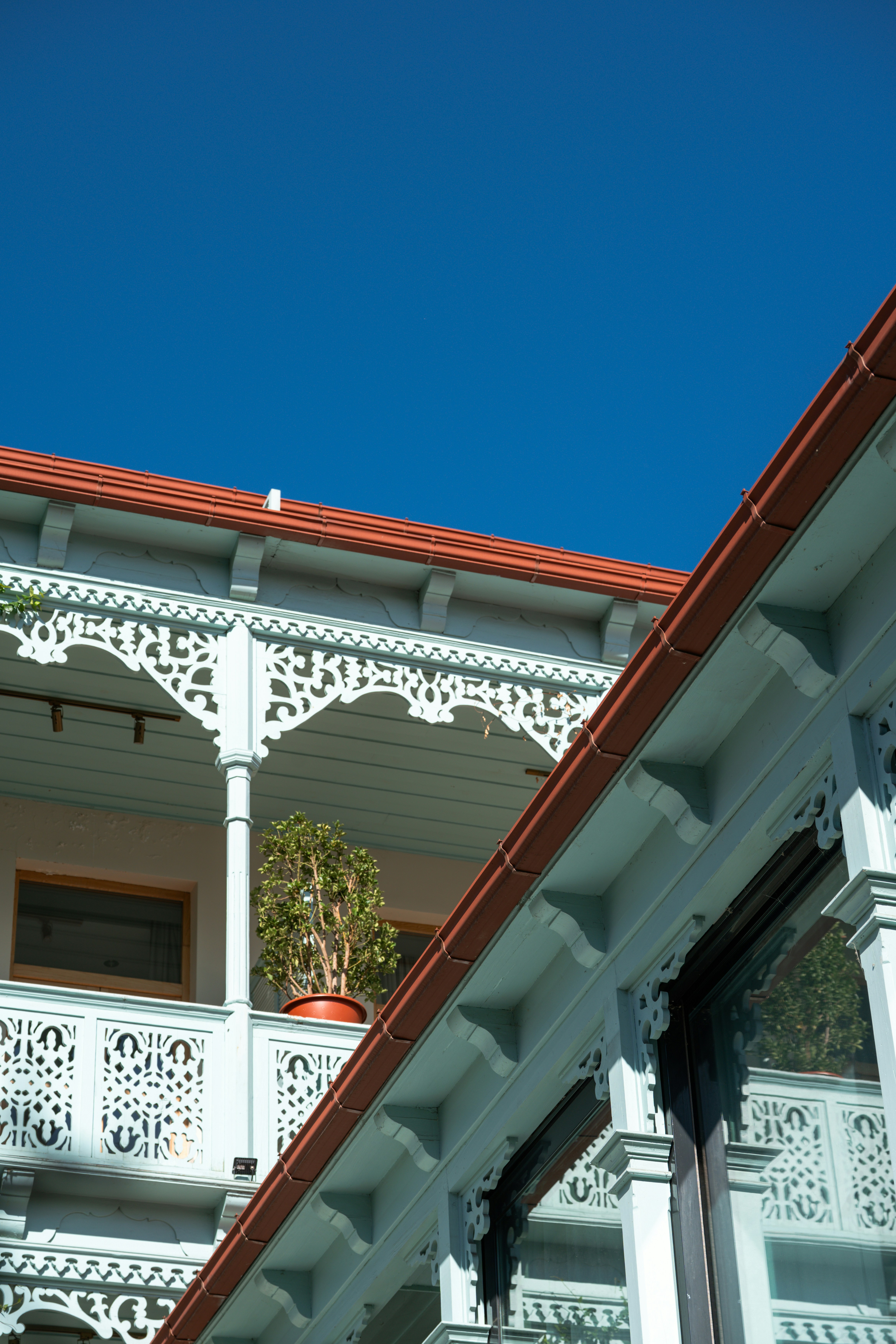 Intricate architectural details of a historic building's balcony with vibrant green foliage and a bright blue sky above.