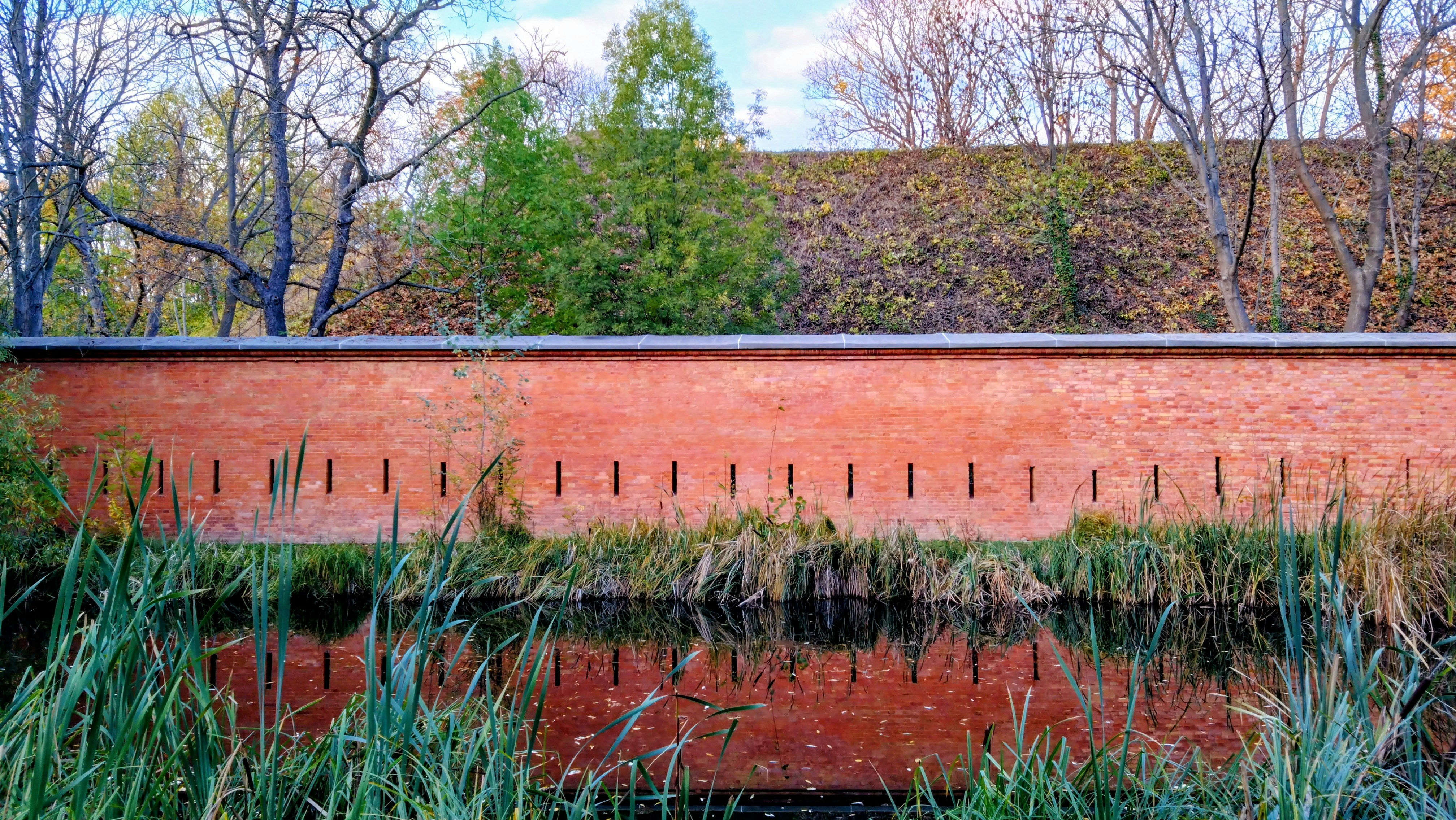 Red brick wall with trees and a pond