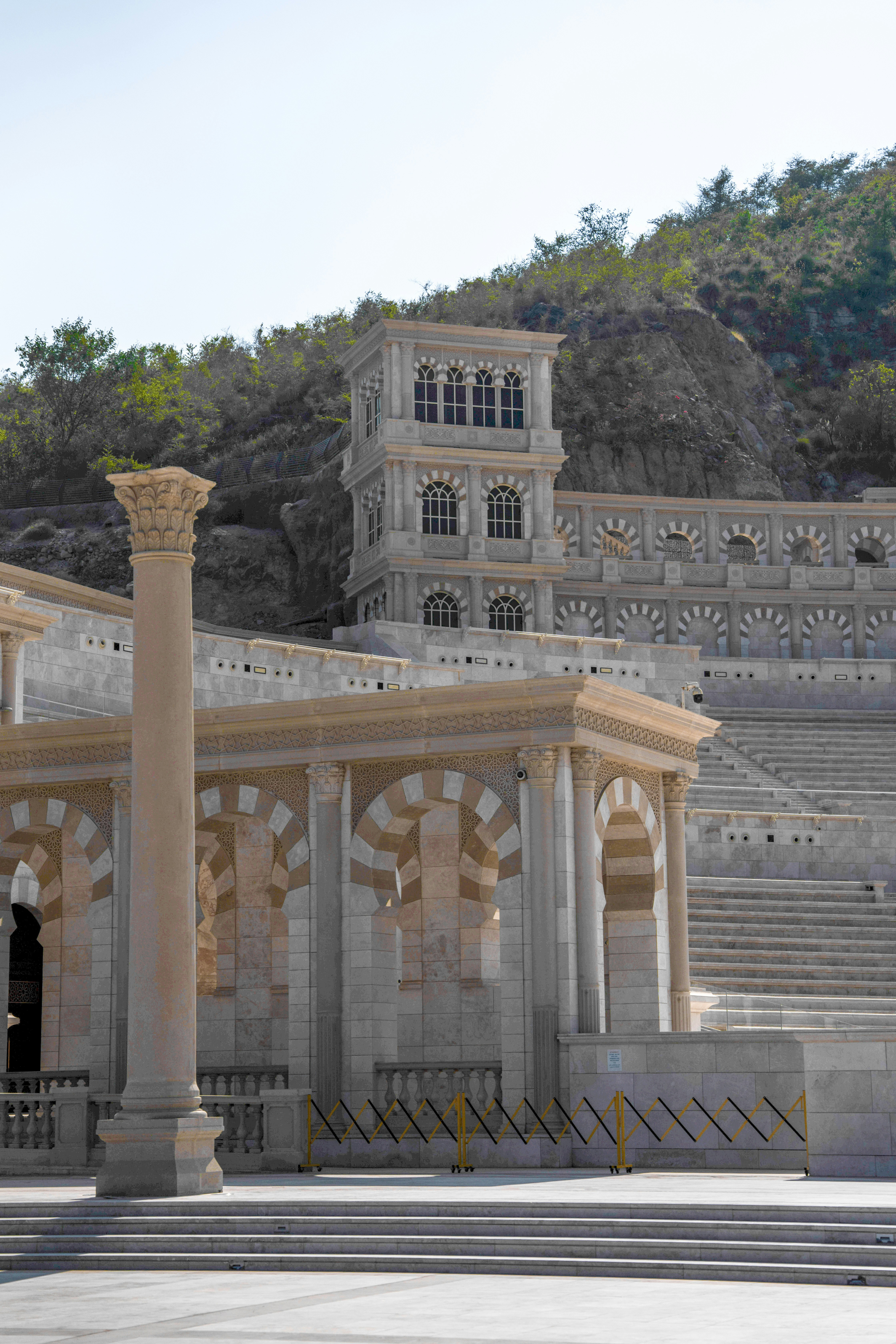 Intricate stone architecture featuring columns and arches set against a hillside backdrop, showcasing careful design and craftsmanship.