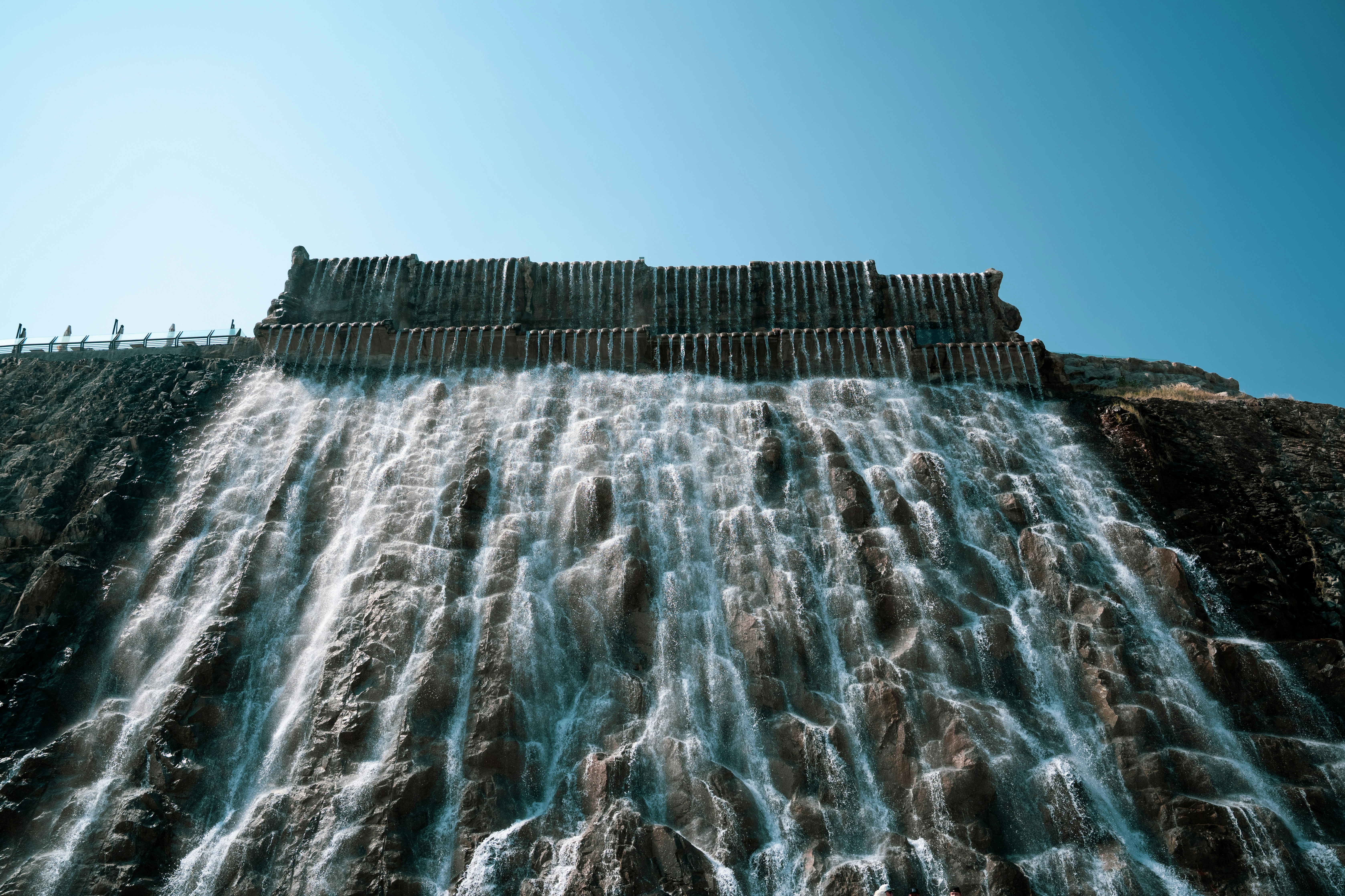Water cascading over a dam, showcasing the power of nature and engineering. The clear blue sky enhances the scene's vibrancy.