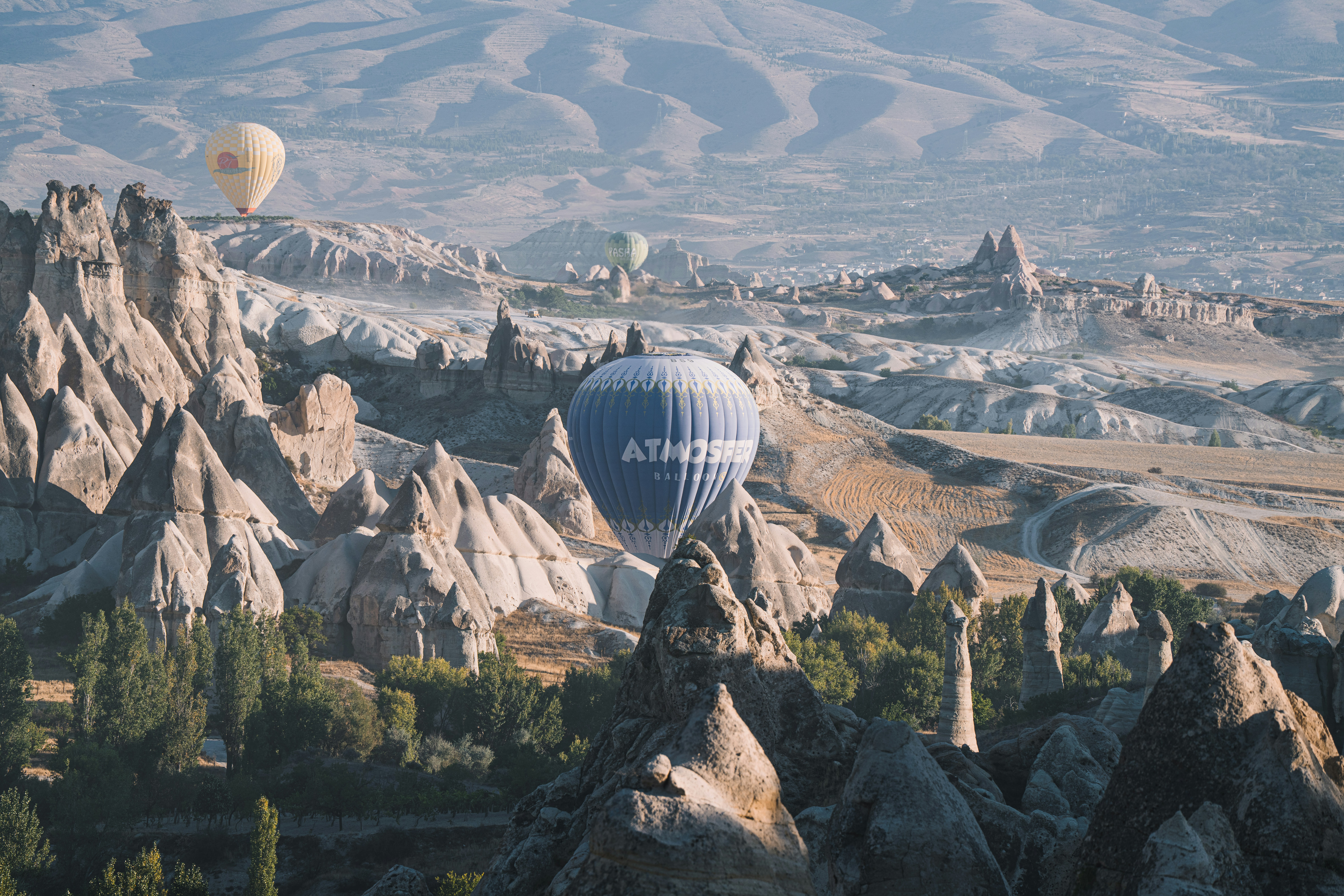 Colorful hot air balloons soar over Cappadocia's surreal rock formations at dawn, creating a whimsical scene. The natural beauty and man-made wonders blend harmoniously.